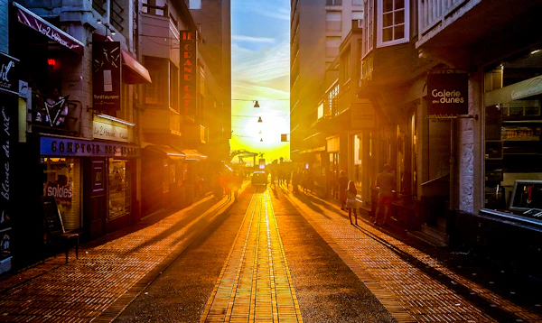 Sunlit cobblestone street between tall buildings at sunset.