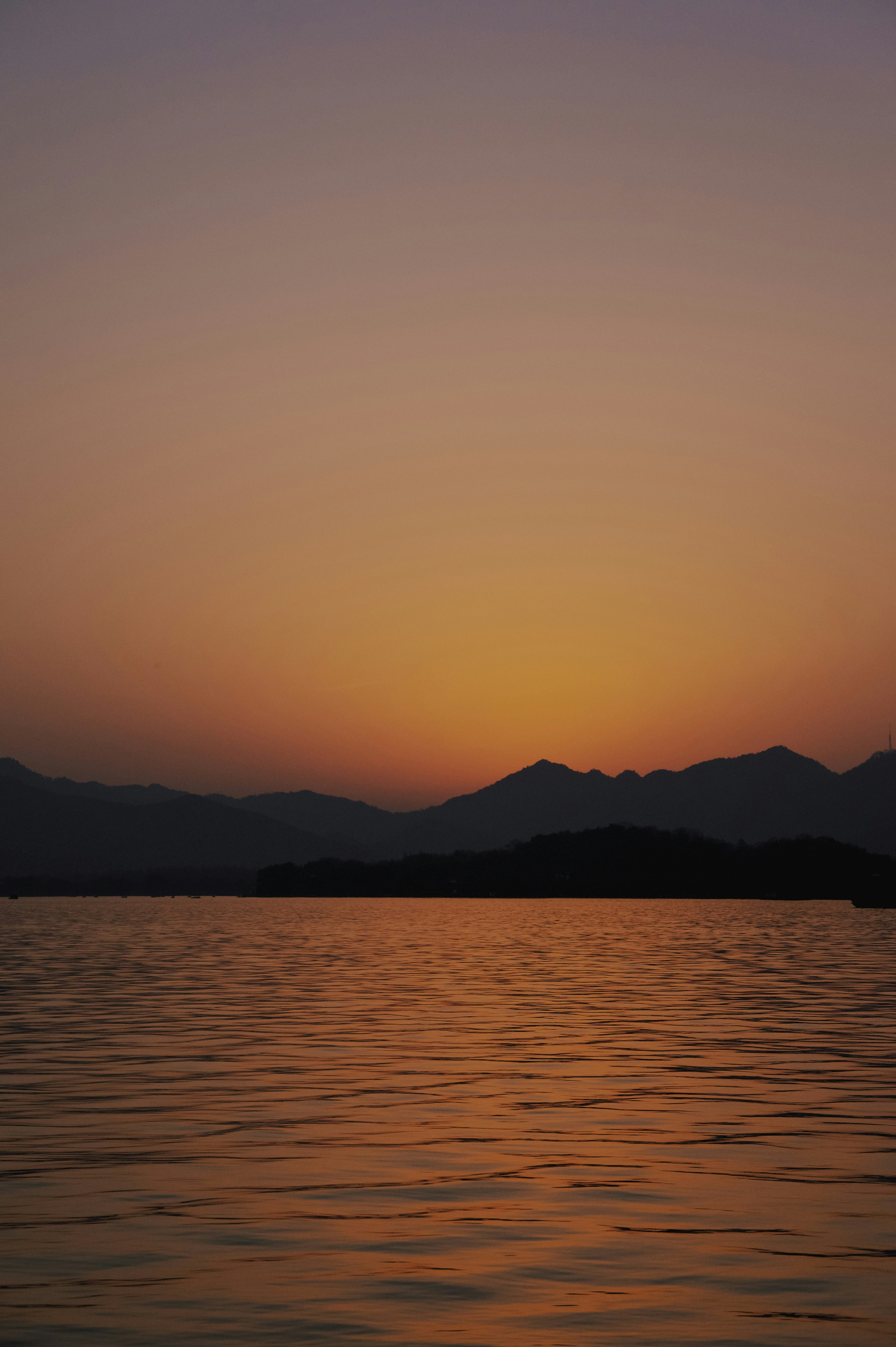 Golden sunset casting warm hues over tranquil lake with distant mountains silhouetted against the sky.