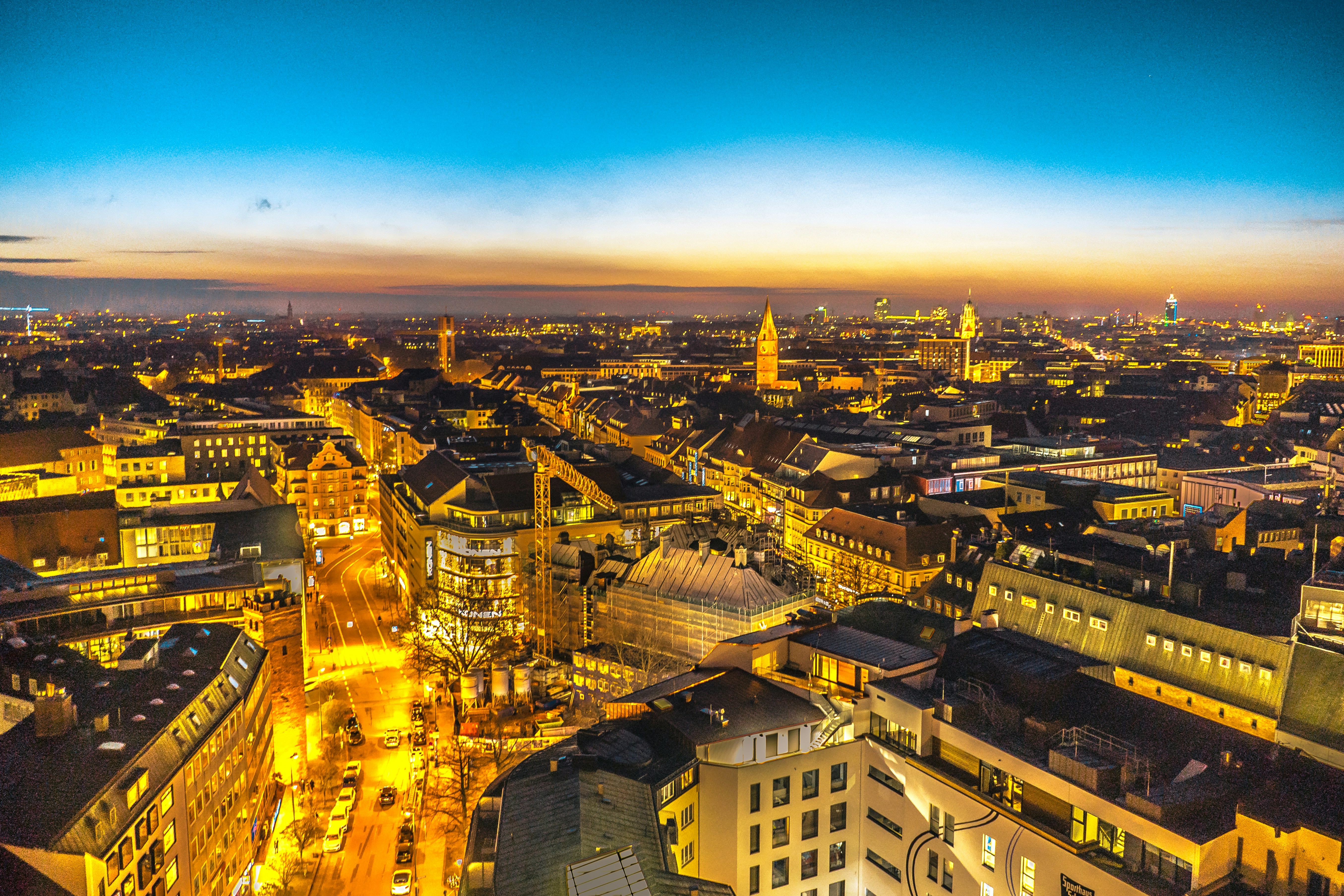 City skyline at dusk with glowing lights and a vivid blue sky.