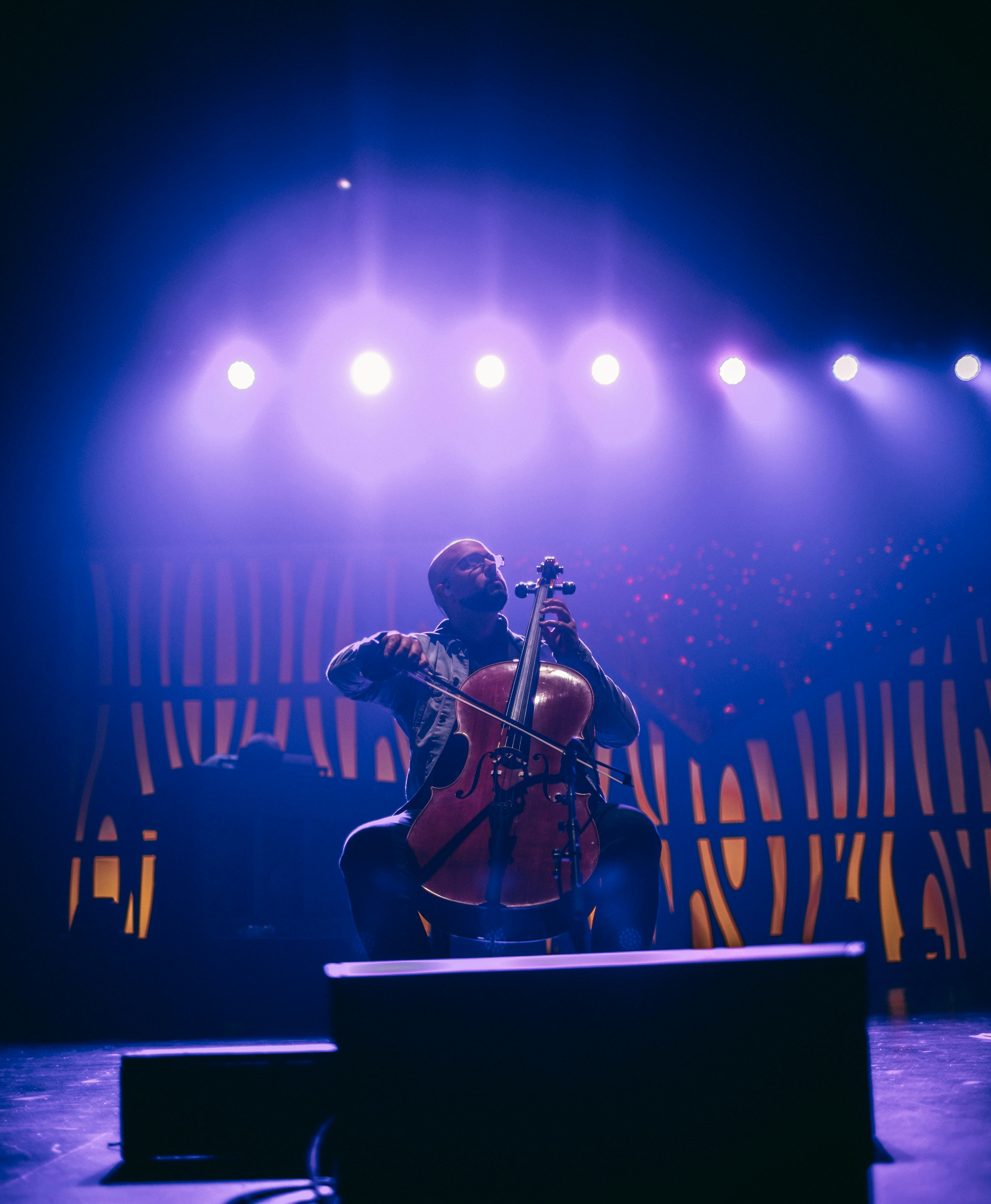 A cellist passionately performing on stage, illuminated by vibrant stage lights, with a dynamic backdrop enhancing the atmosphere.