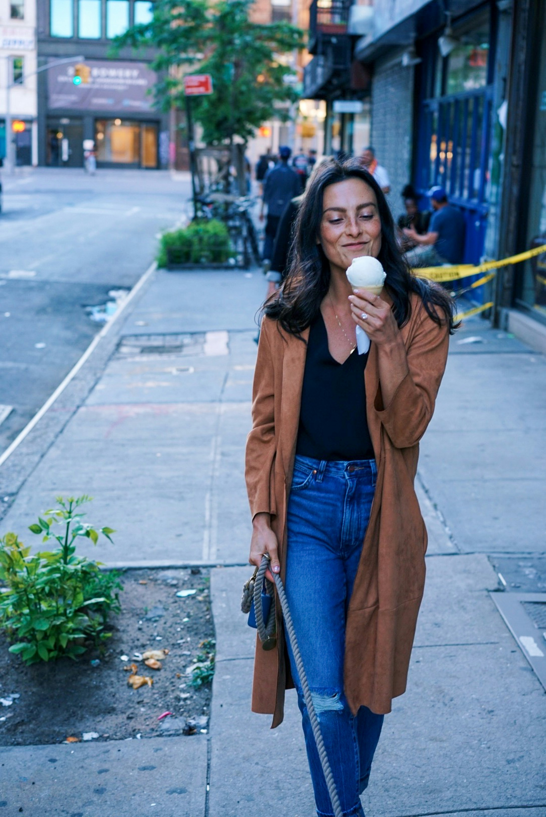 Woman enjoying an ice cream cone while strolling down a city sidewalk, surrounded by urban life.