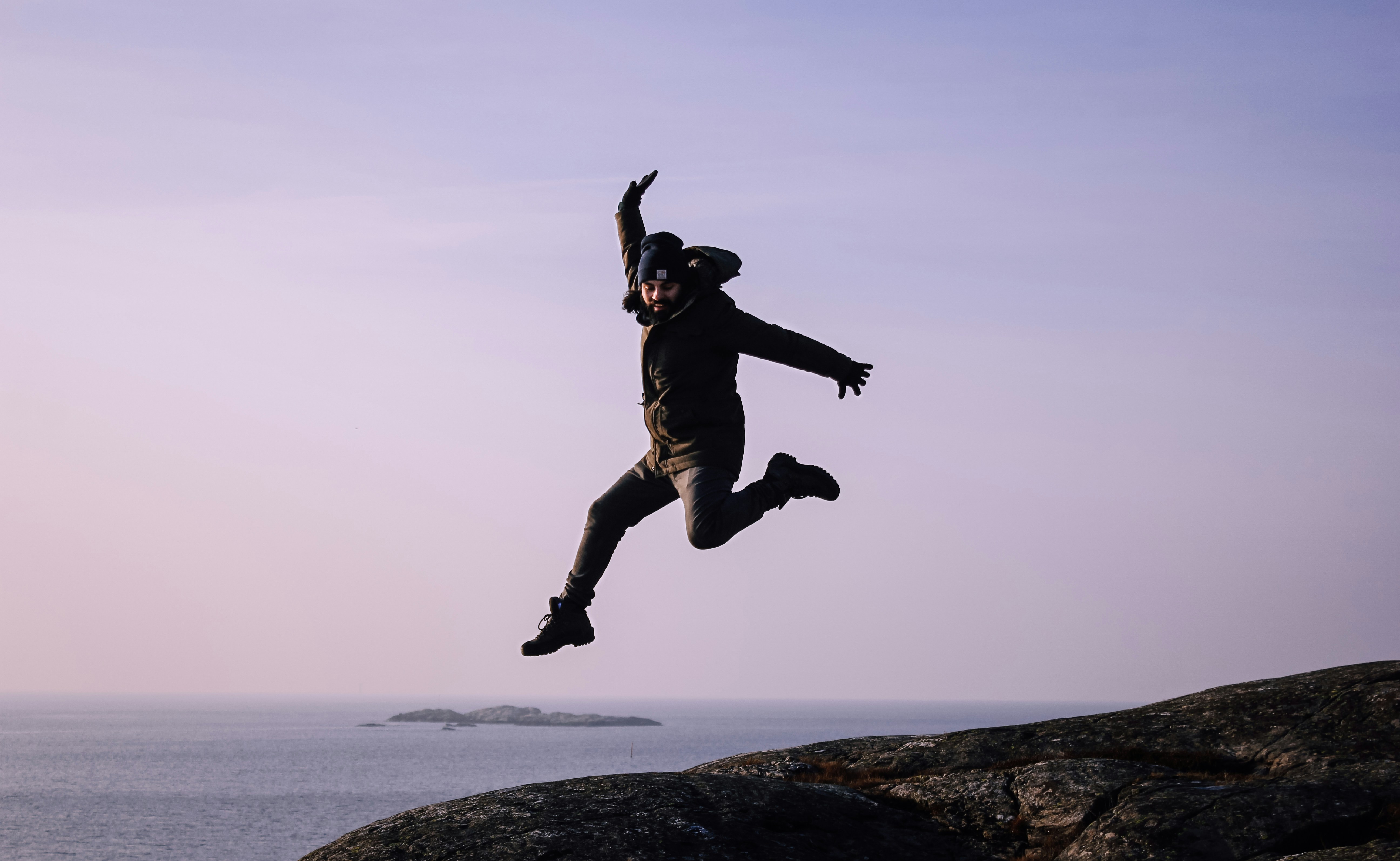 Silhouette of a person mid-jump on coastal rocks against a pastel sky.