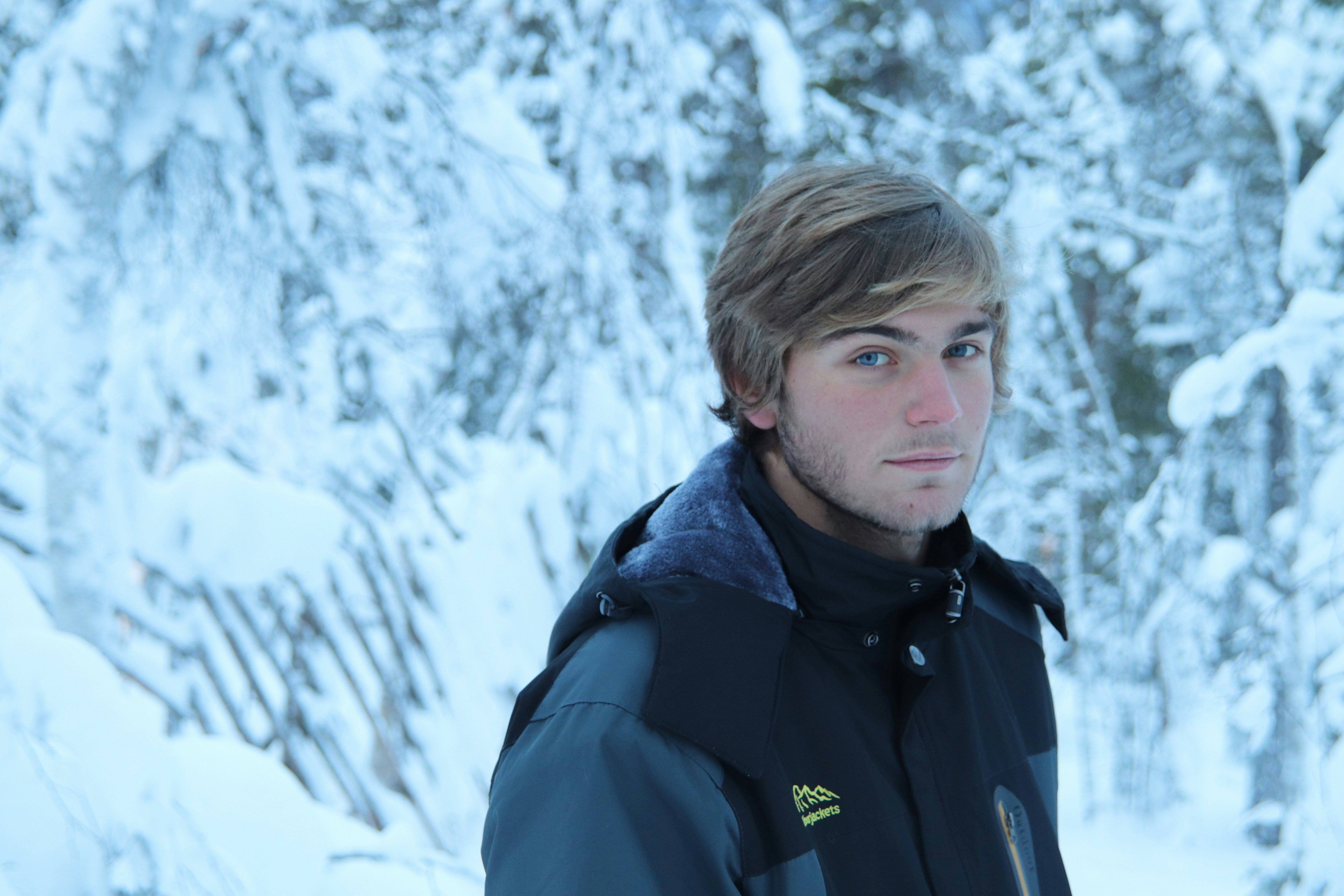 Young man stands amidst a snowy landscape, capturing the serene essence of winter. His contemplative gaze contrasts with the frosty surroundings.