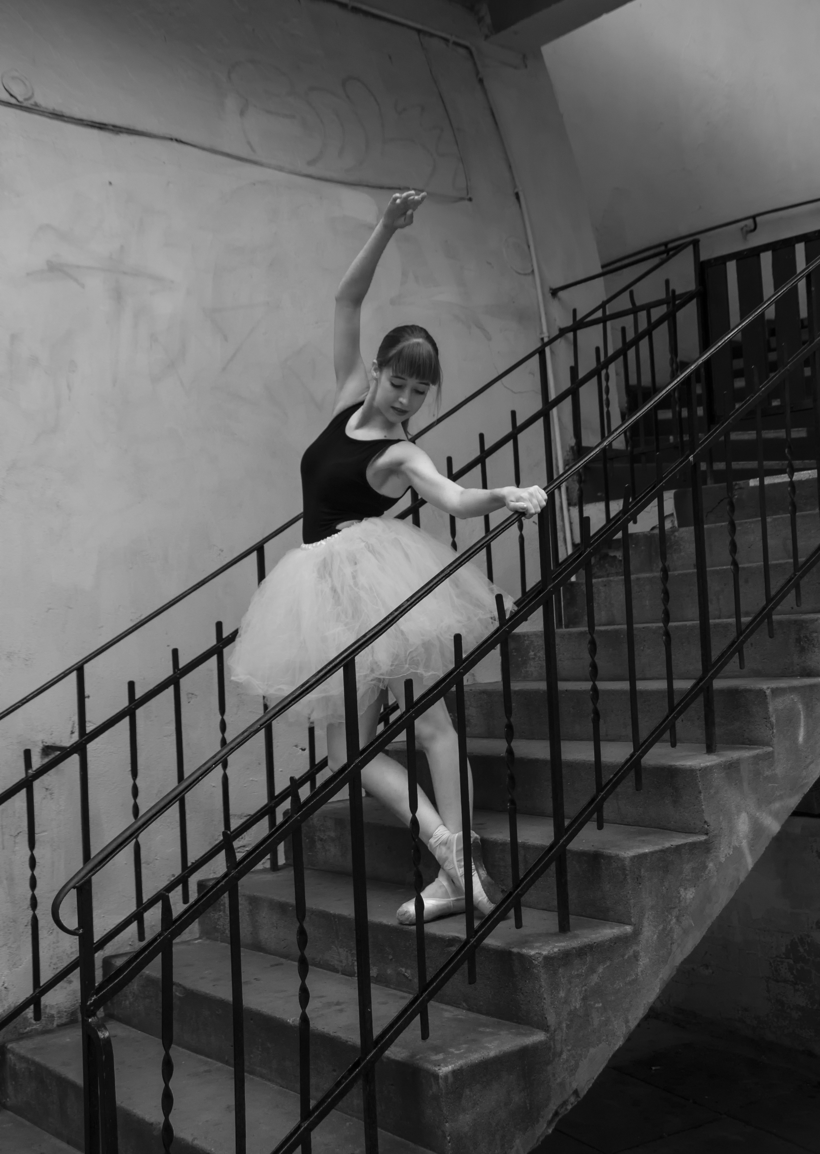 Ballet dancer gracefully poses on a staircase, showcasing fluidity and strength in her movement. The monochrome tones emphasize the elegance of her attire and form.