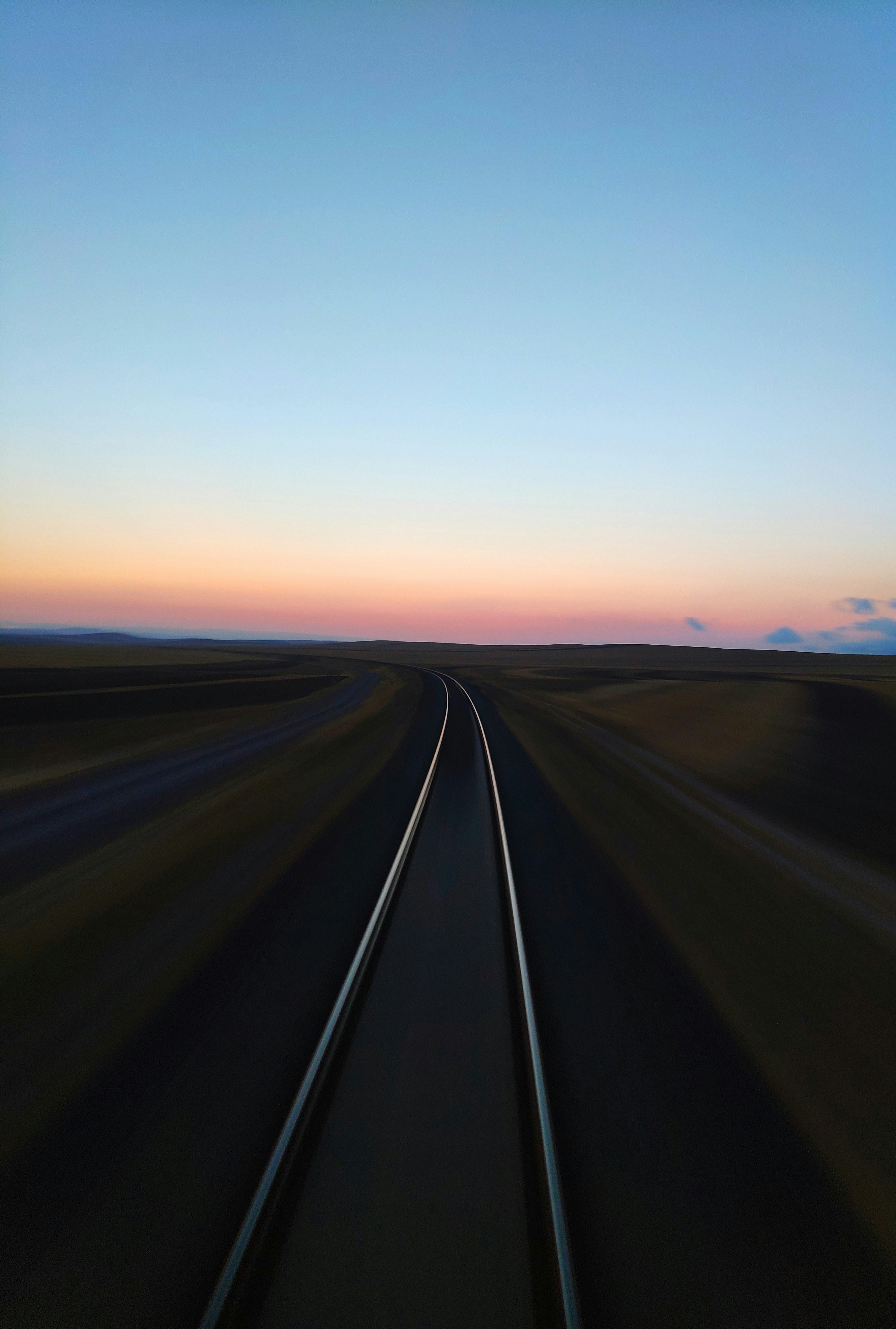 Curving railway tracks lead towards a pastel-colored horizon at dusk, evoking a sense of adventure and exploration.