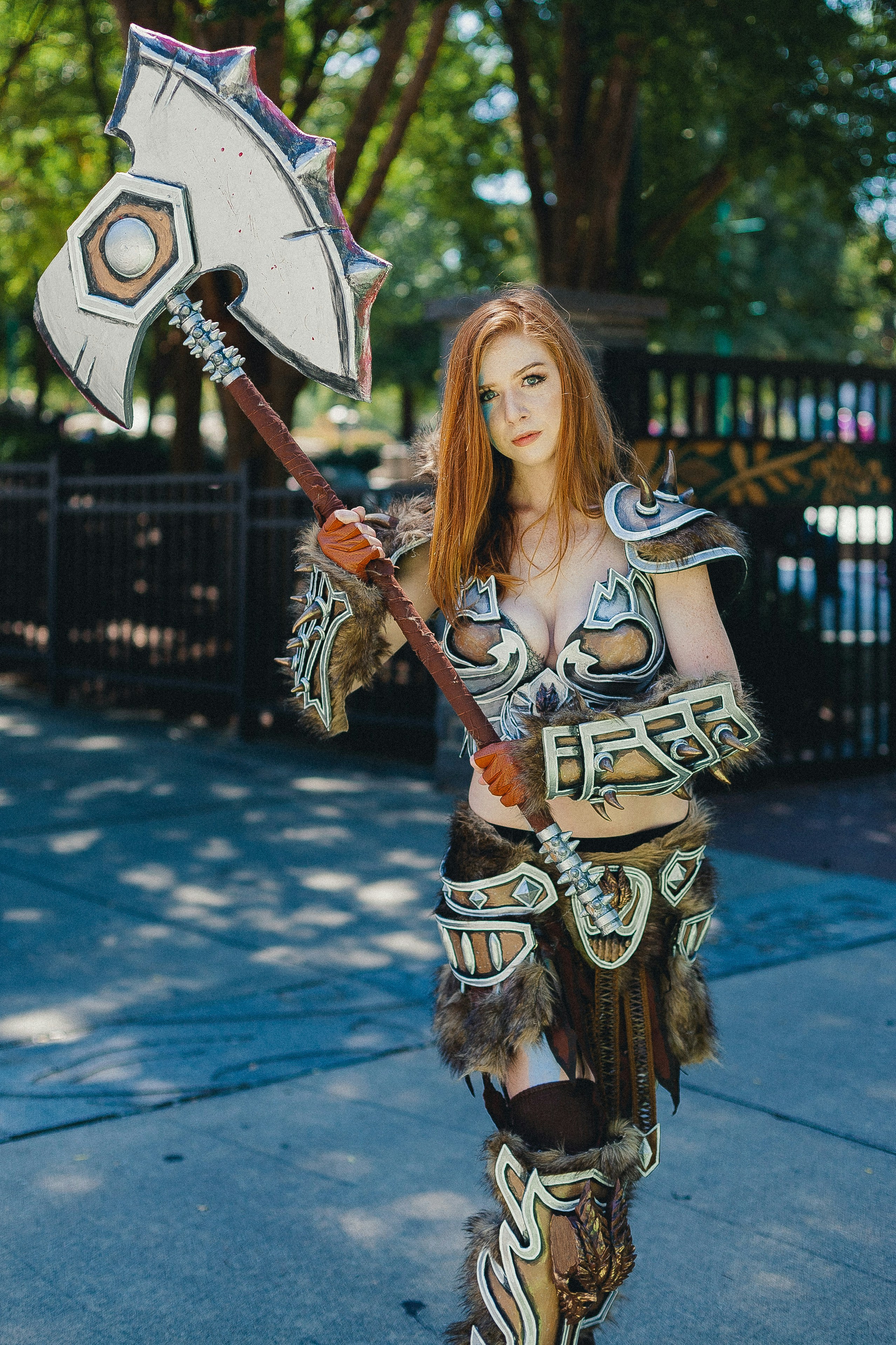 Cosplayer dressed as a fierce warrior, wielding a large axe, showcasing intricate armor details in a vibrant outdoor setting.