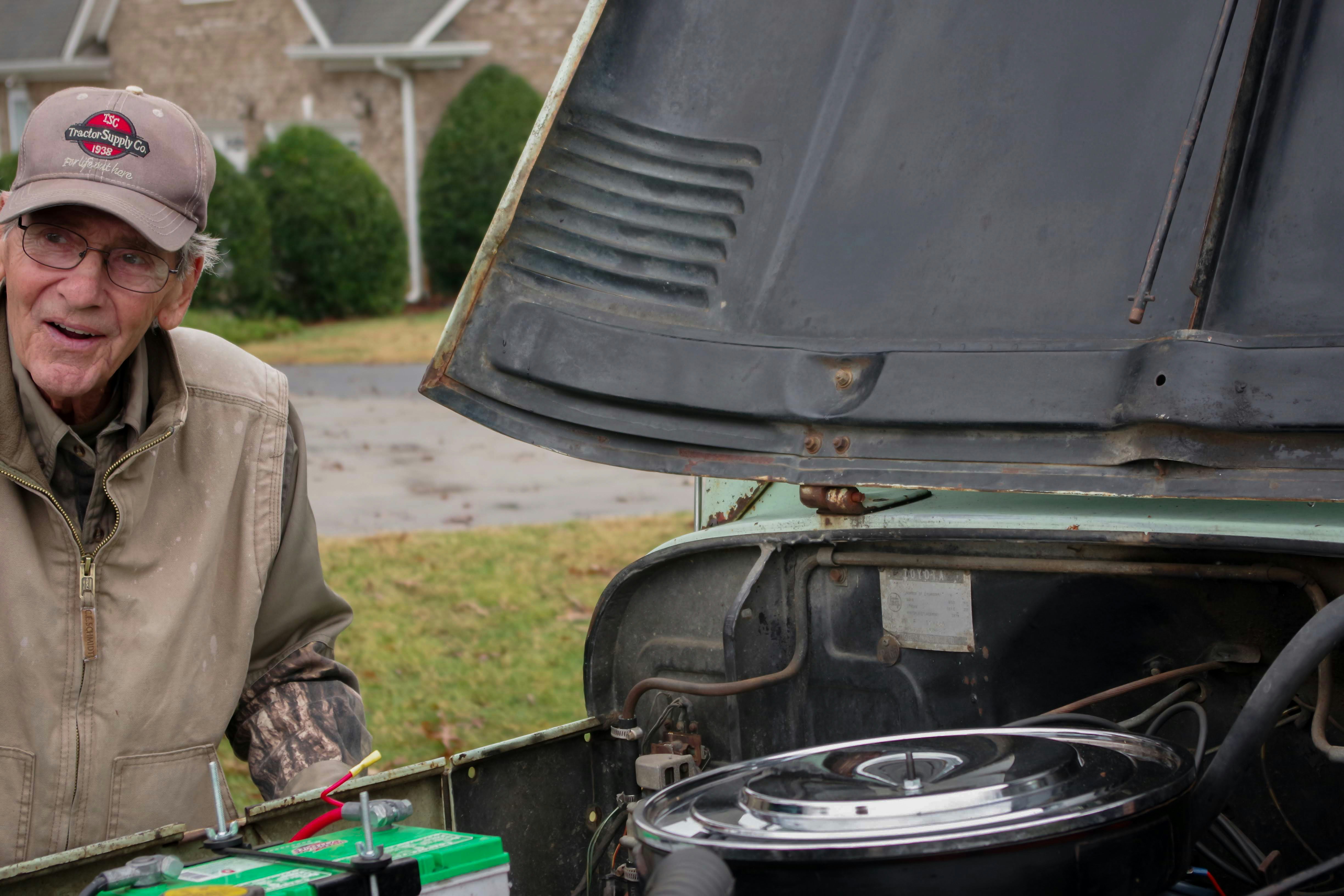 Old mechanic at the open car hood, a moment of quiet repair beneath a suburban sky