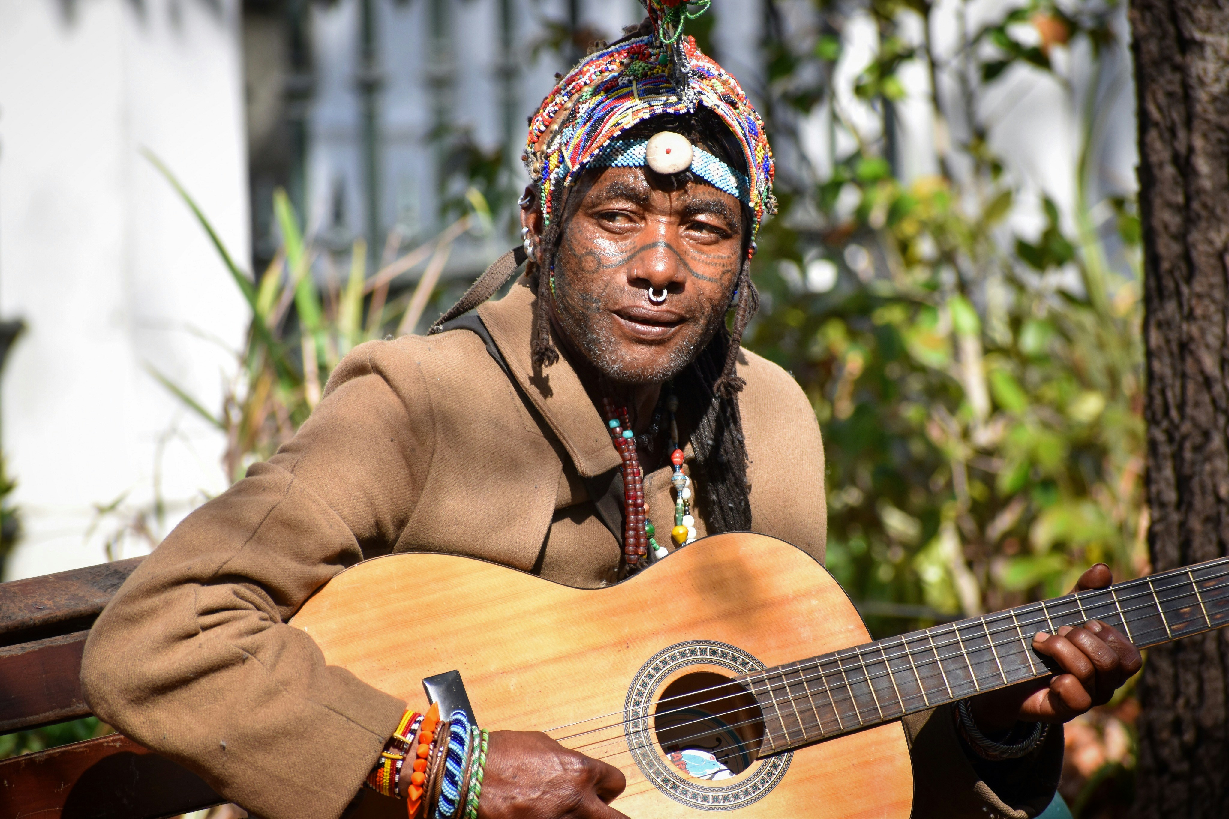 A musician with intricate facial tattoos and vibrant accessories strums a guitar, embodying the spirit of street art and culture.