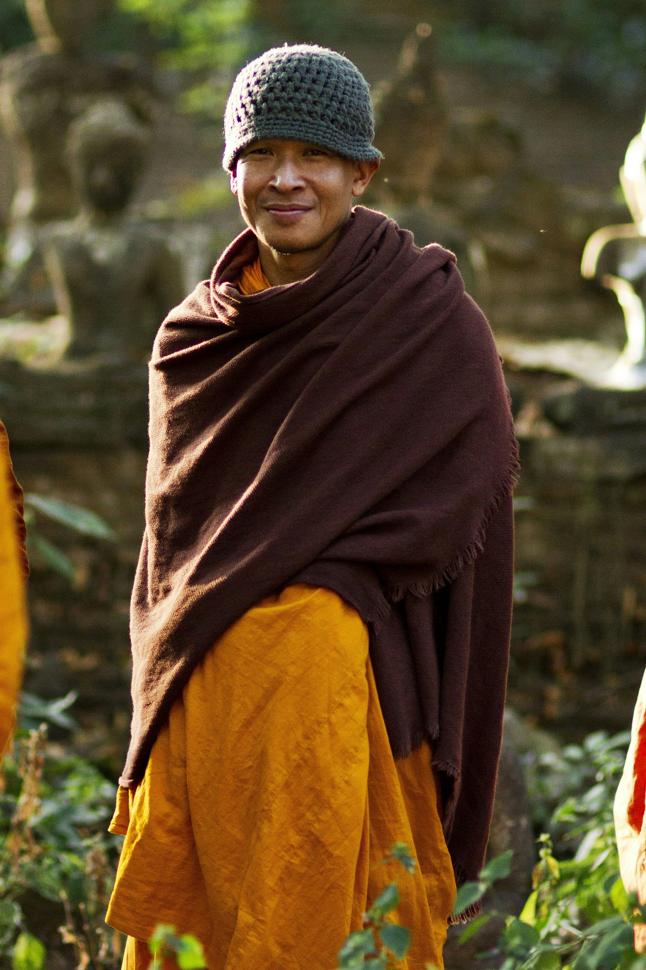 Monk dressed in traditional robes stands amidst ancient stone statues, exuding tranquility and wisdom.