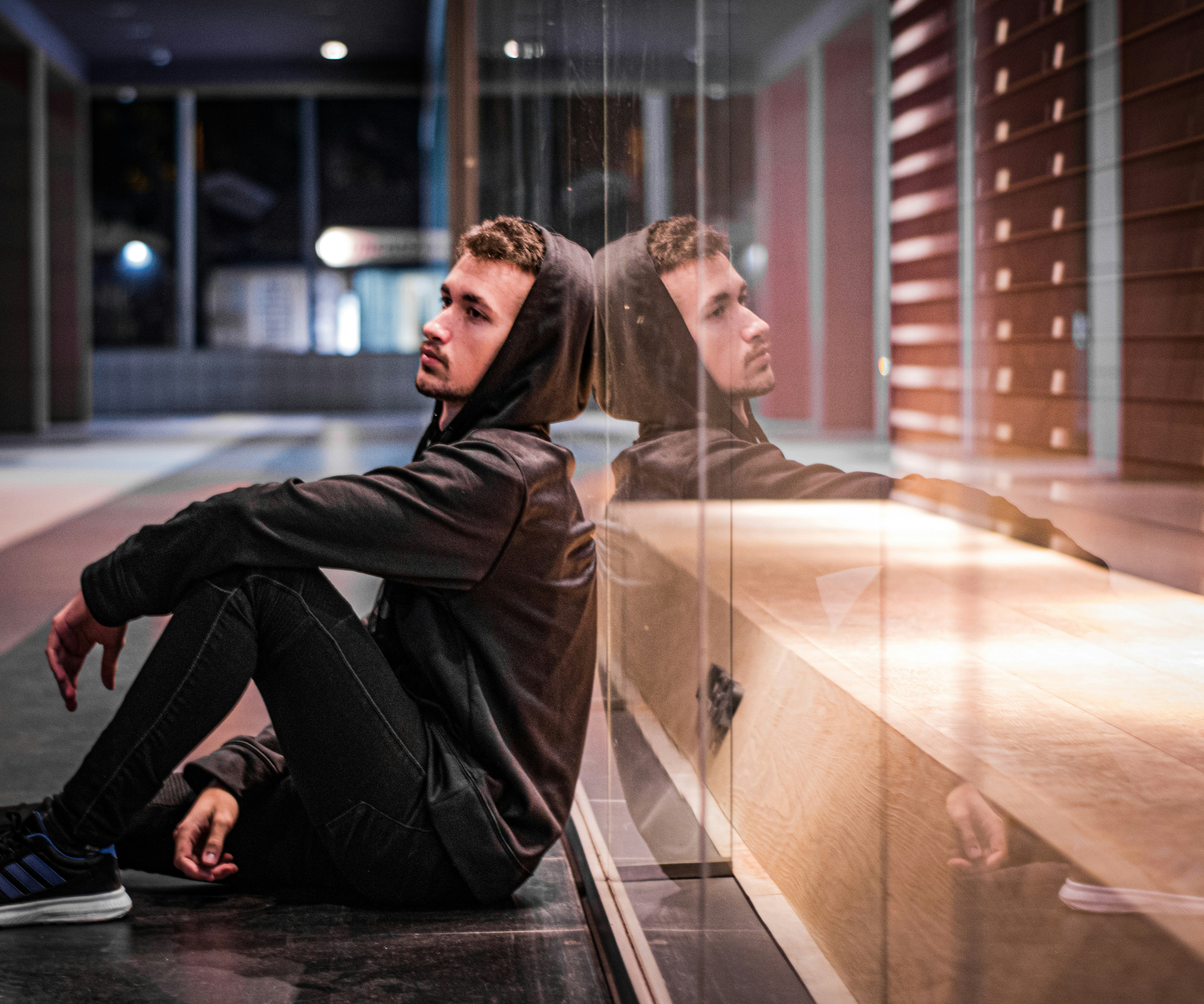 Neon Quiet: A Hoodie-Clad Figure Paused Against a Glass Wall