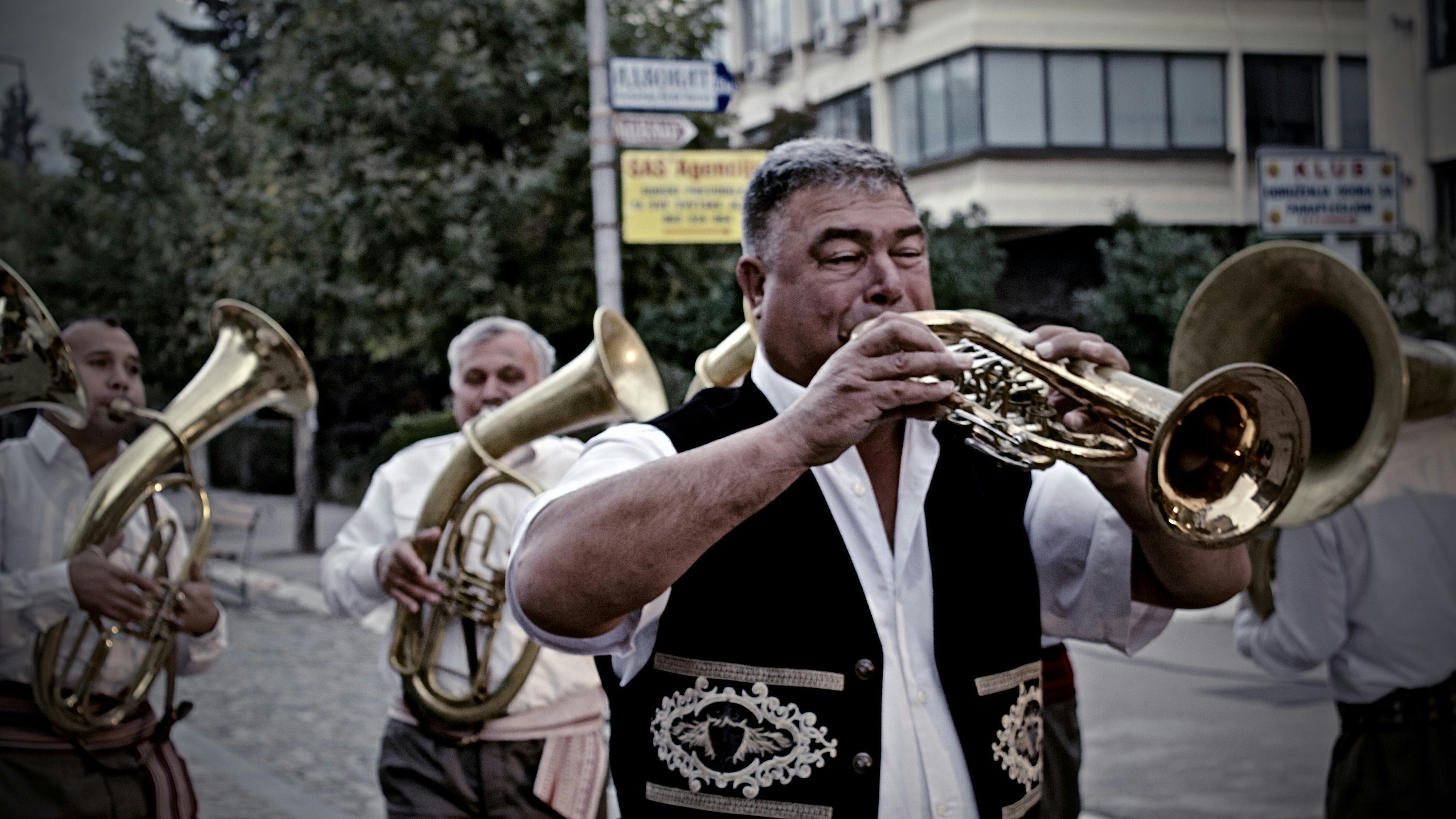 Brass musicians in traditional attire performing energetically on a city street.