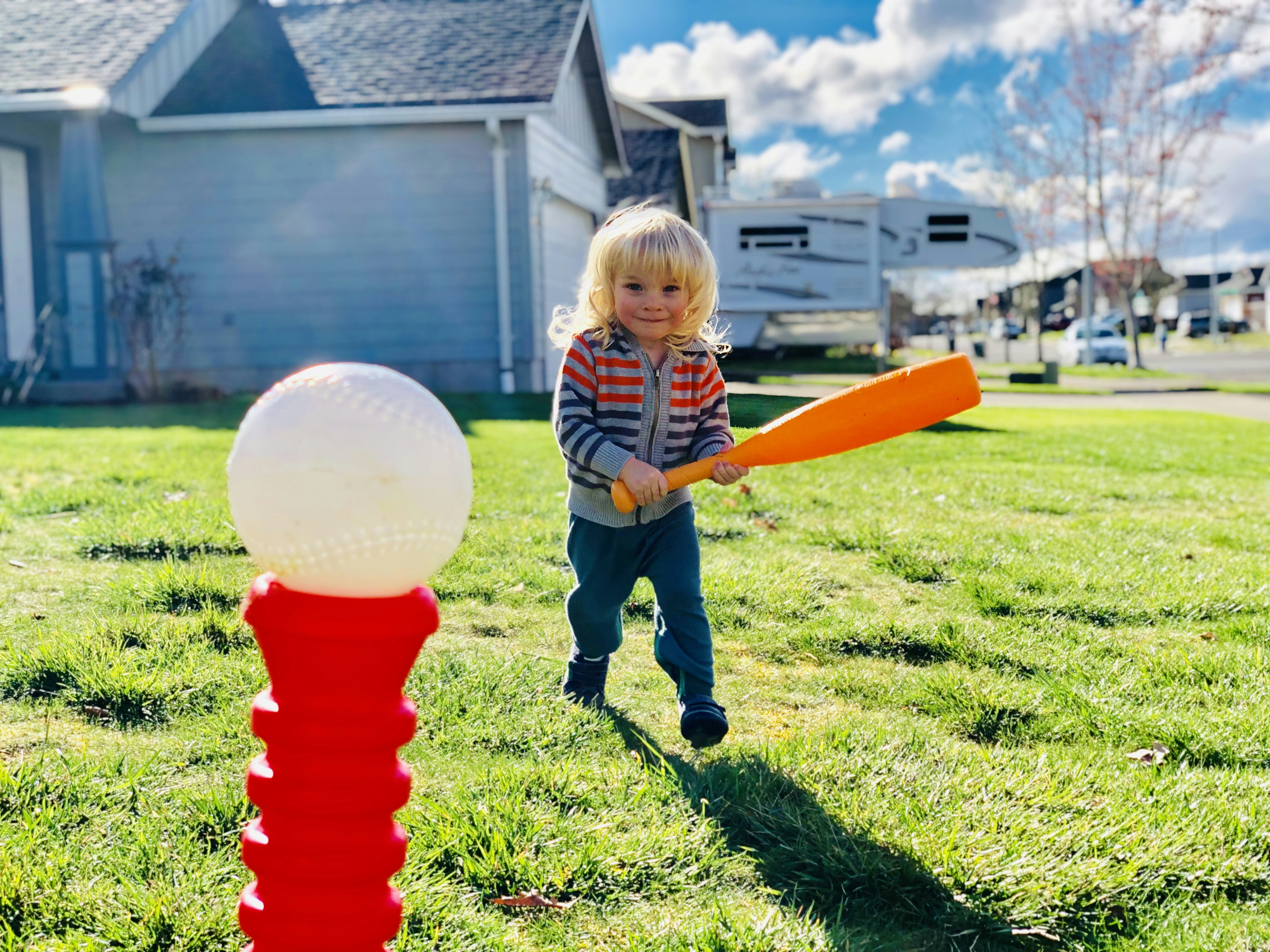 Boy holding orange bat walking toward red and white plastic pole toy ...