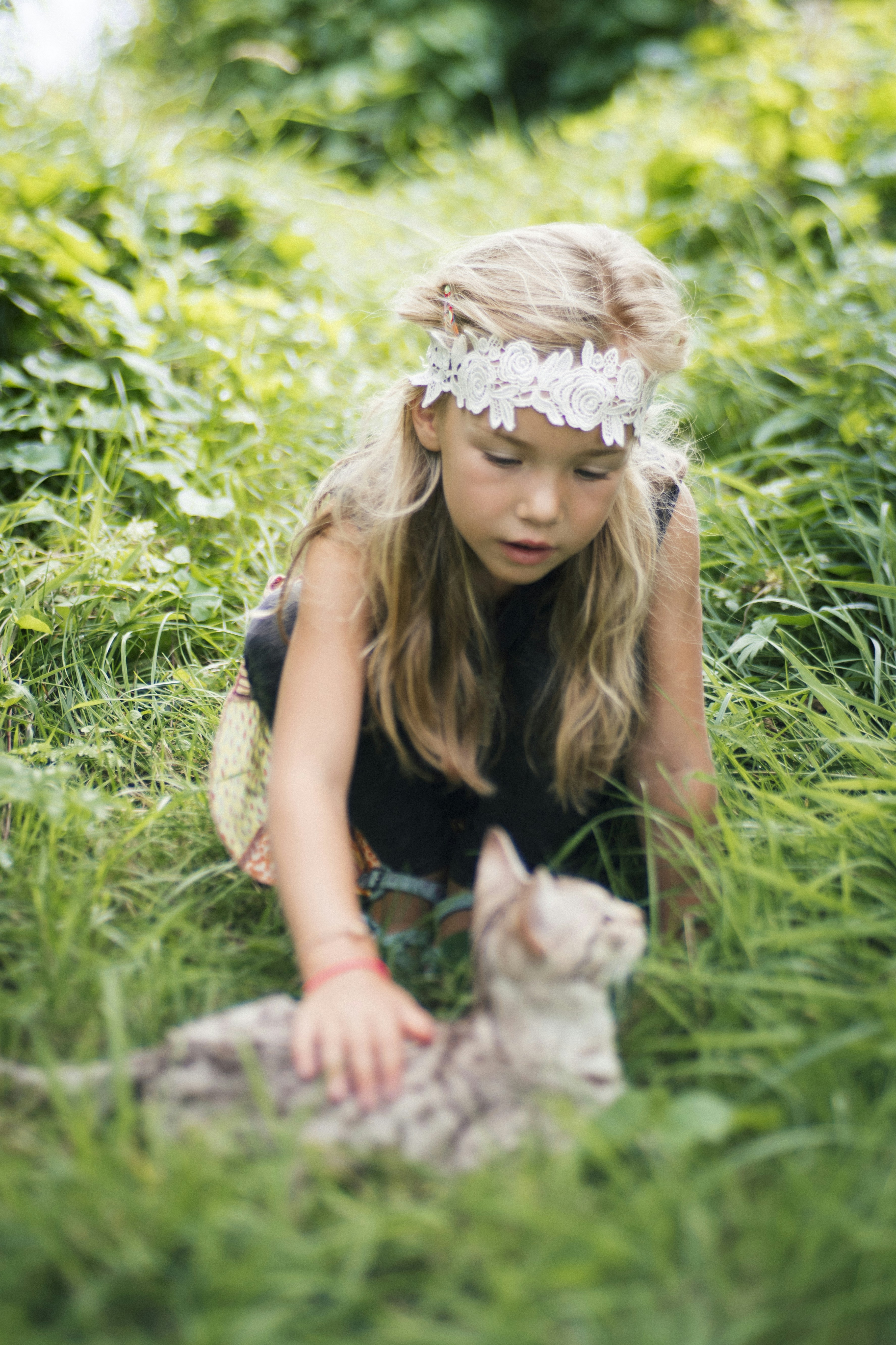 Young girl gently interacting with a cat amidst lush greenery, showcasing a moment of tenderness and curiosity.