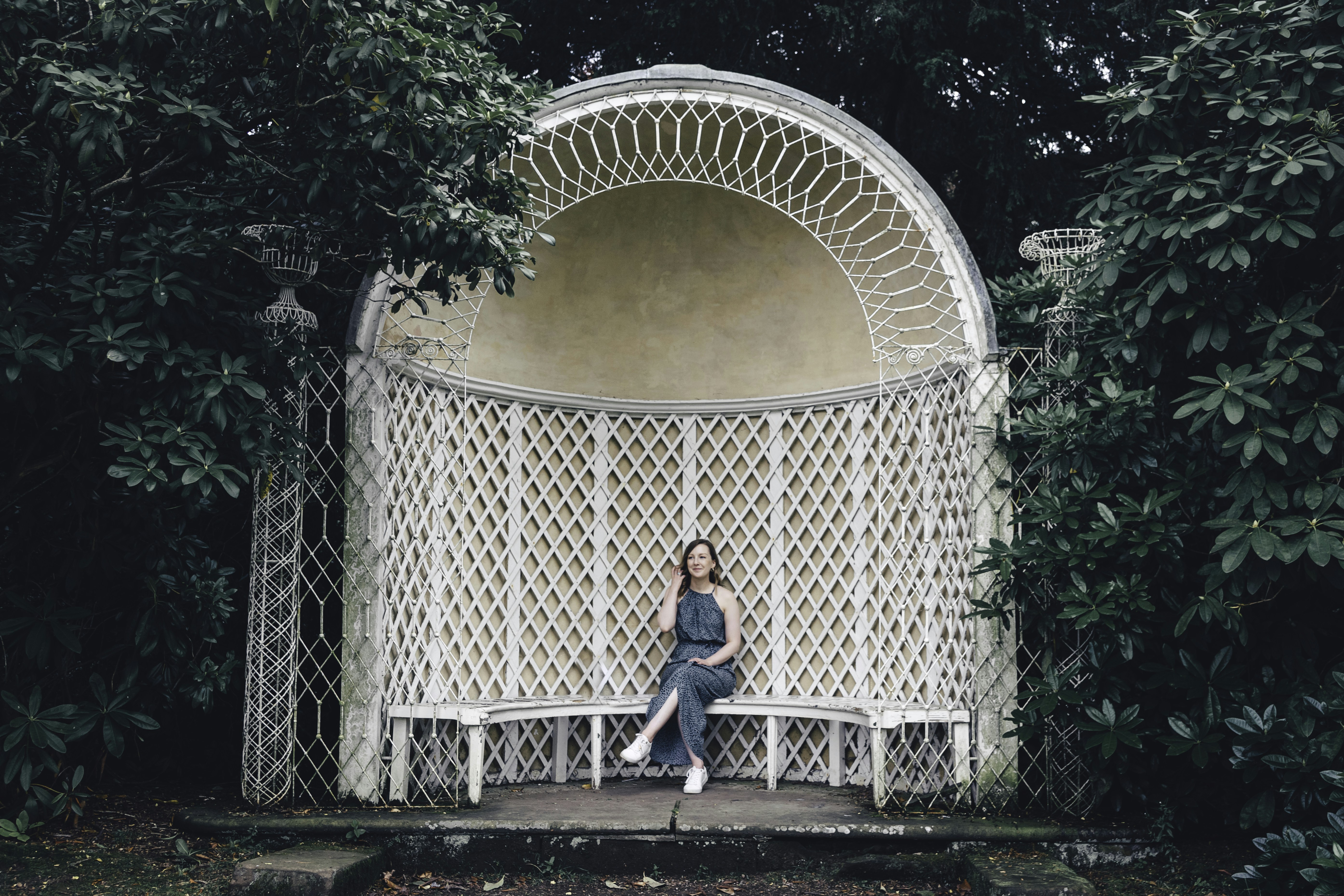 Girl in blue dress sat on a large bench surrounded by foliage