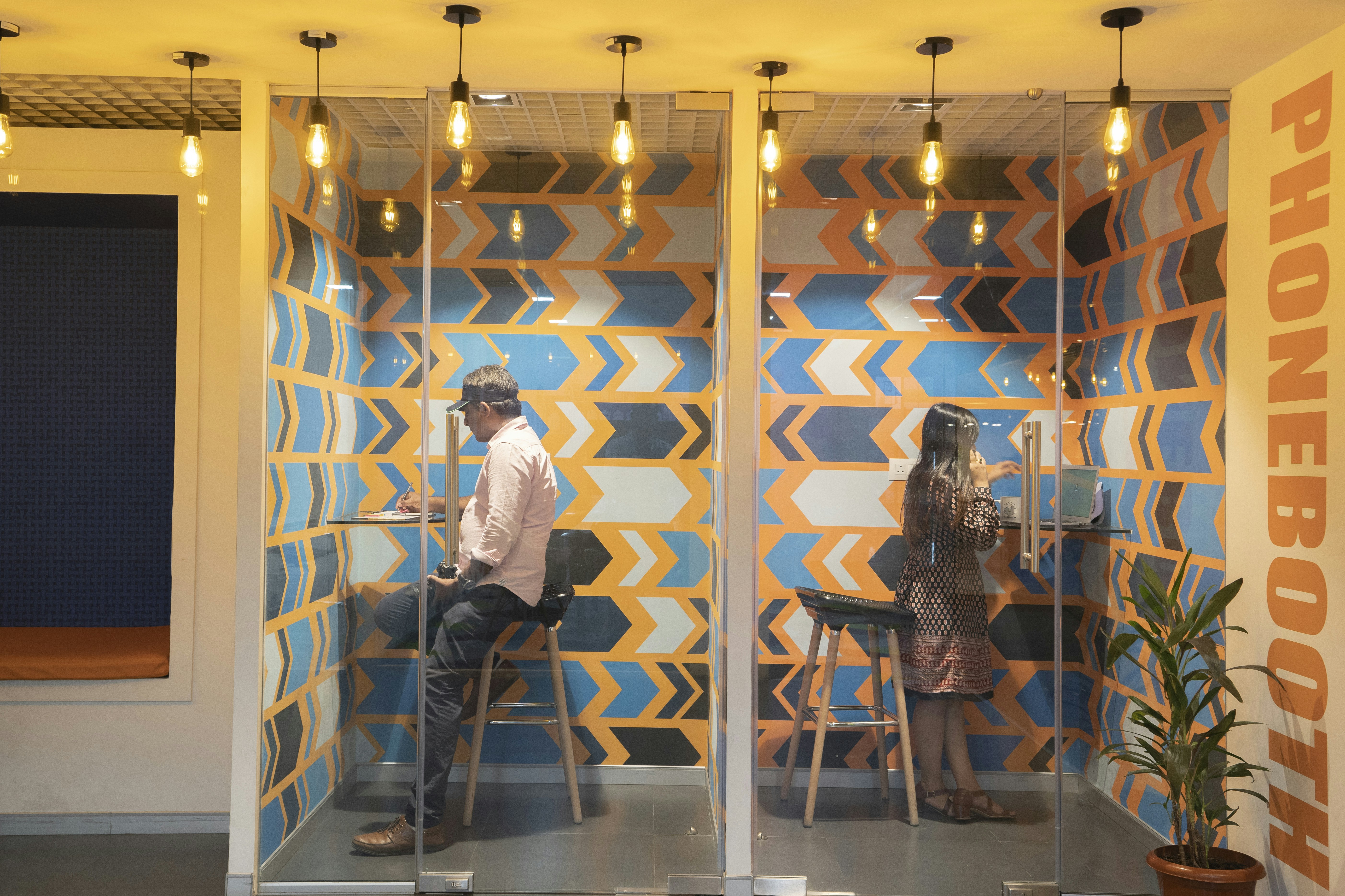 Two individuals seated in colorful phone booths with geometric patterns and warm lighting.