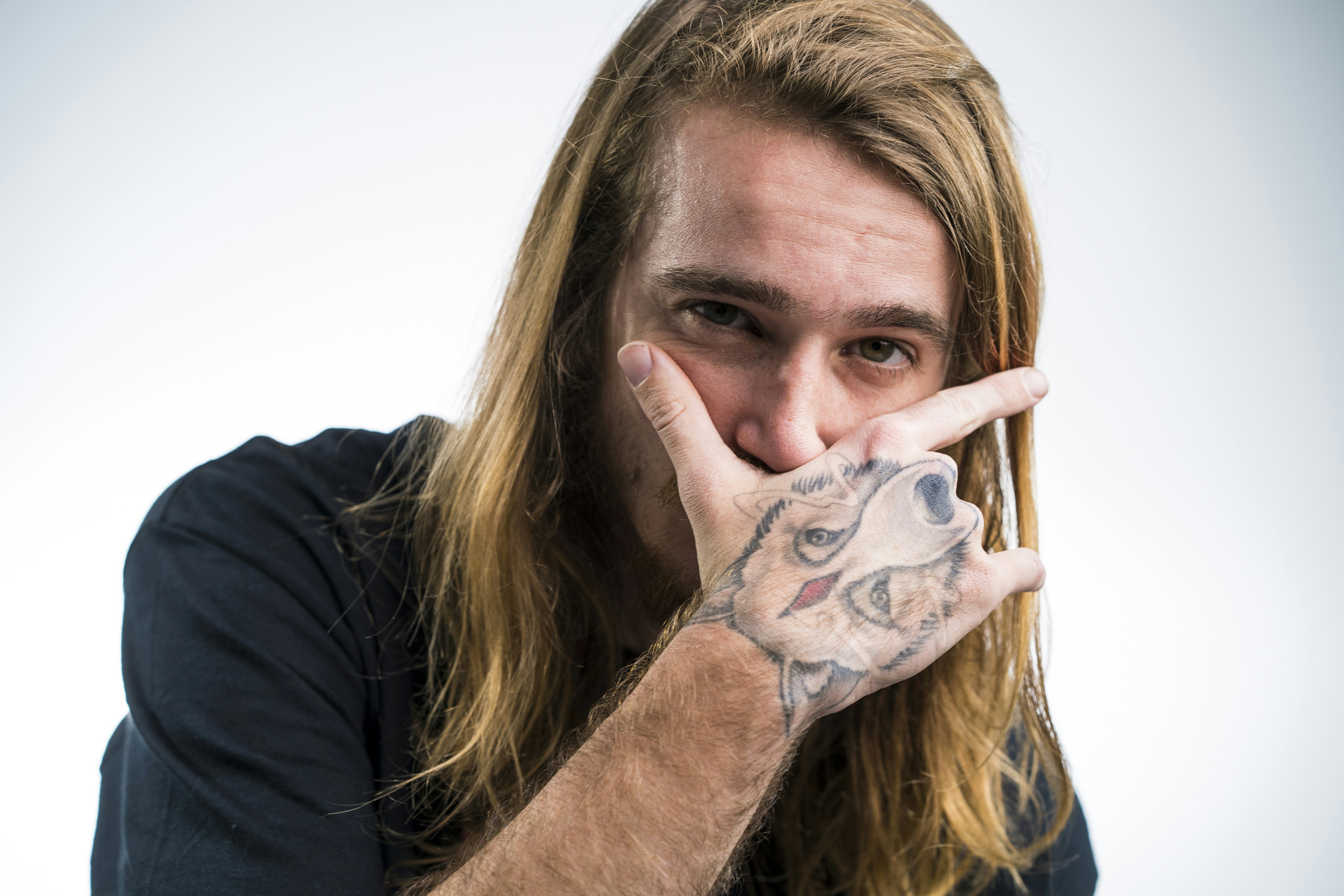 Hand-inked gaze: a man with long blond hair peers through a tattooed hand