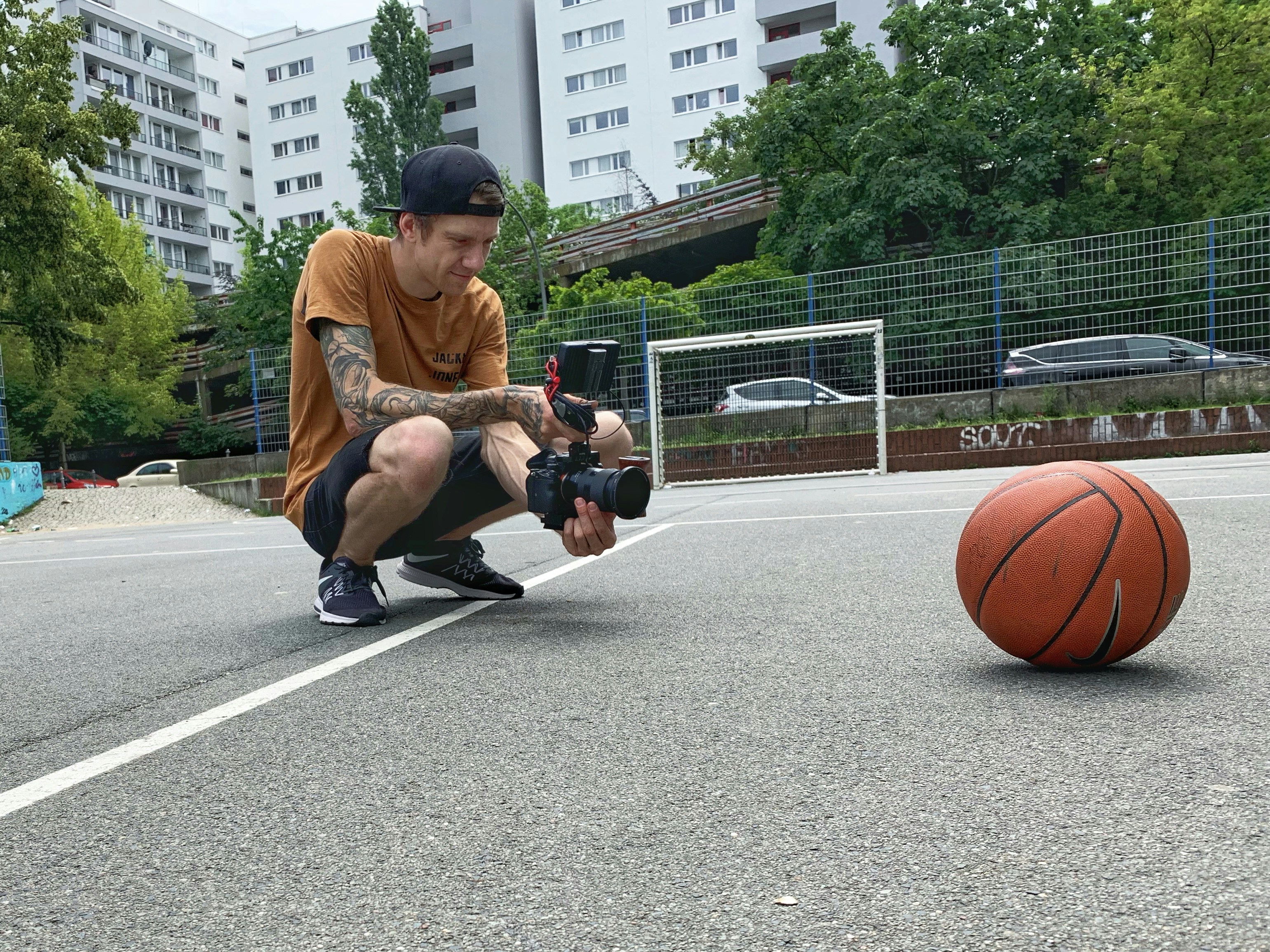 Crouched Lensman on a City Court, Framing a Lone Basketball