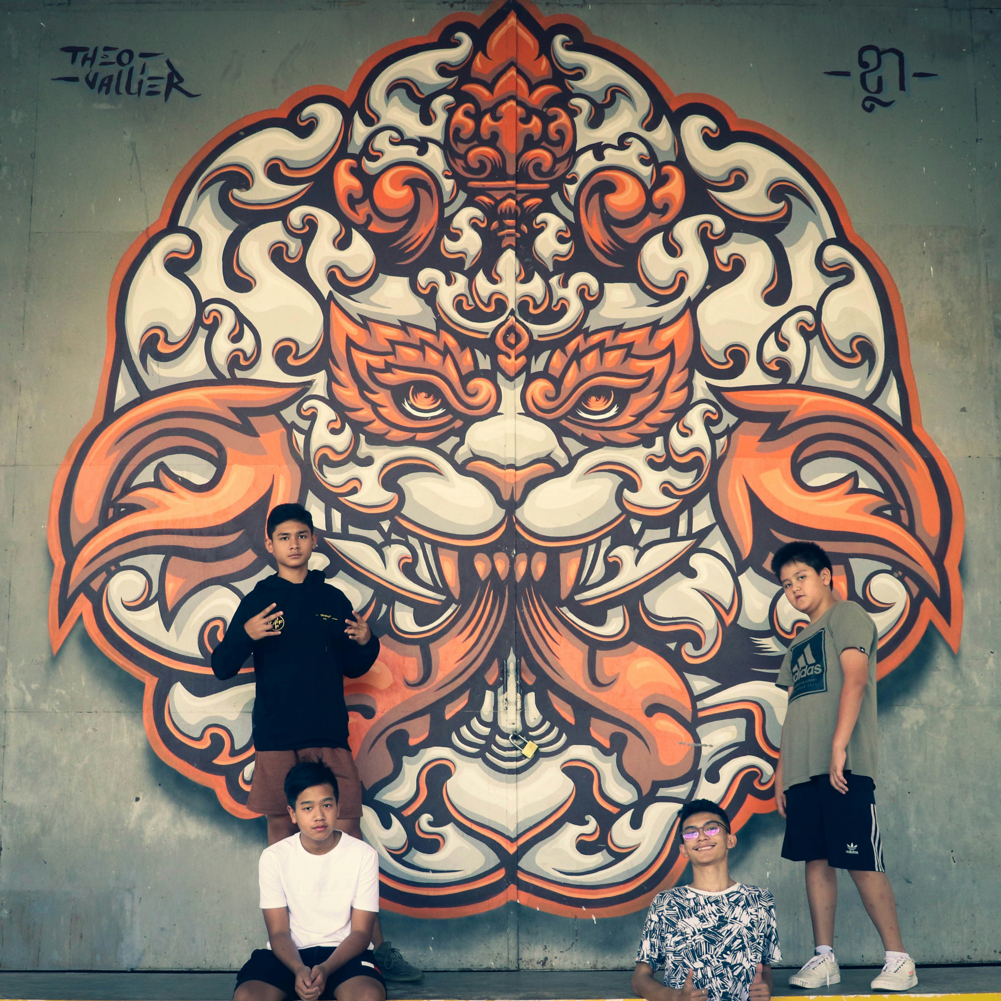 Four young individuals pose in front of a vibrant mural featuring a stylized lion, showcasing urban culture and creativity.