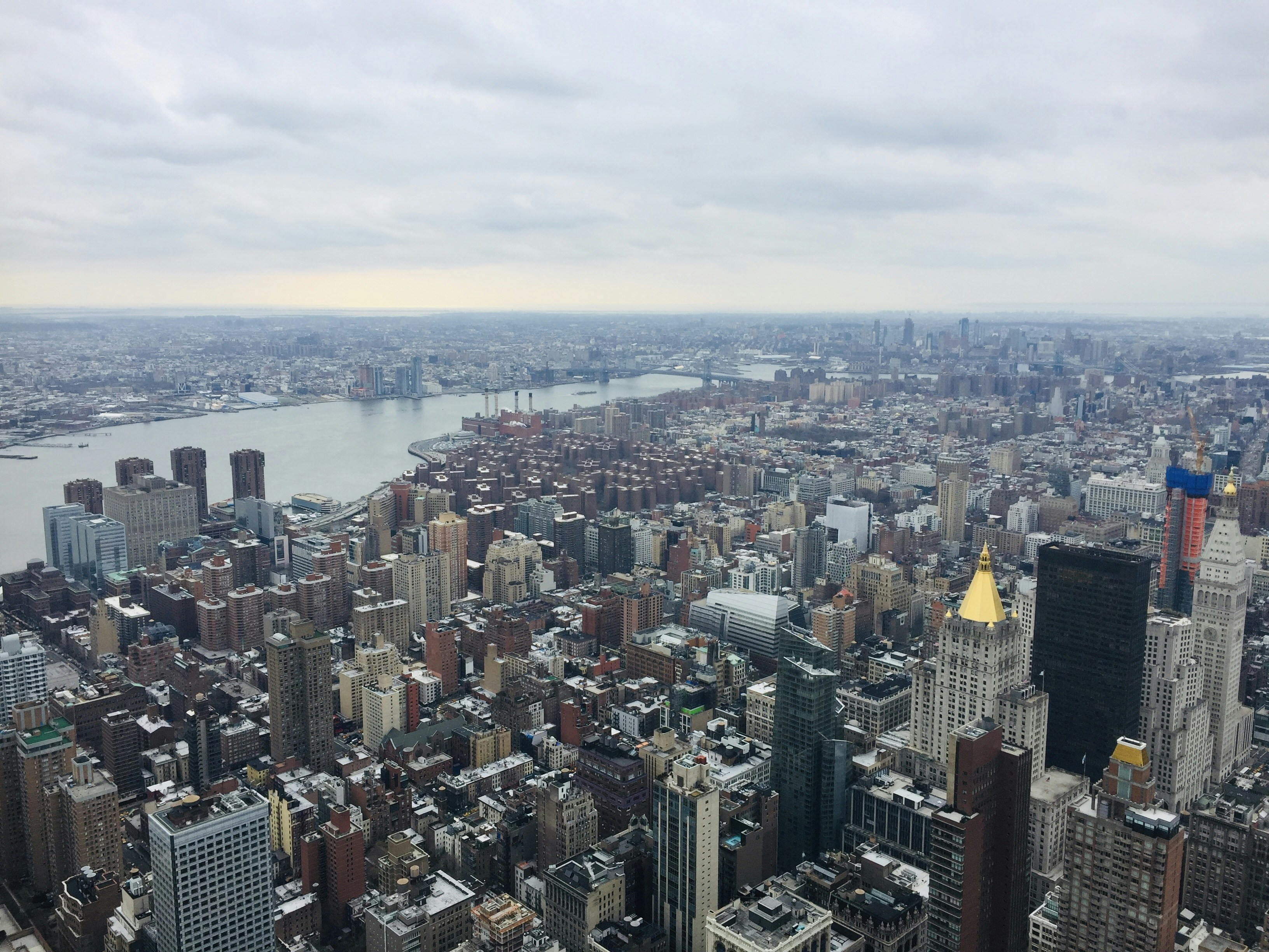 Aerial view of dense cityscape with diverse skyscrapers and a winding river under a cloudy sky.