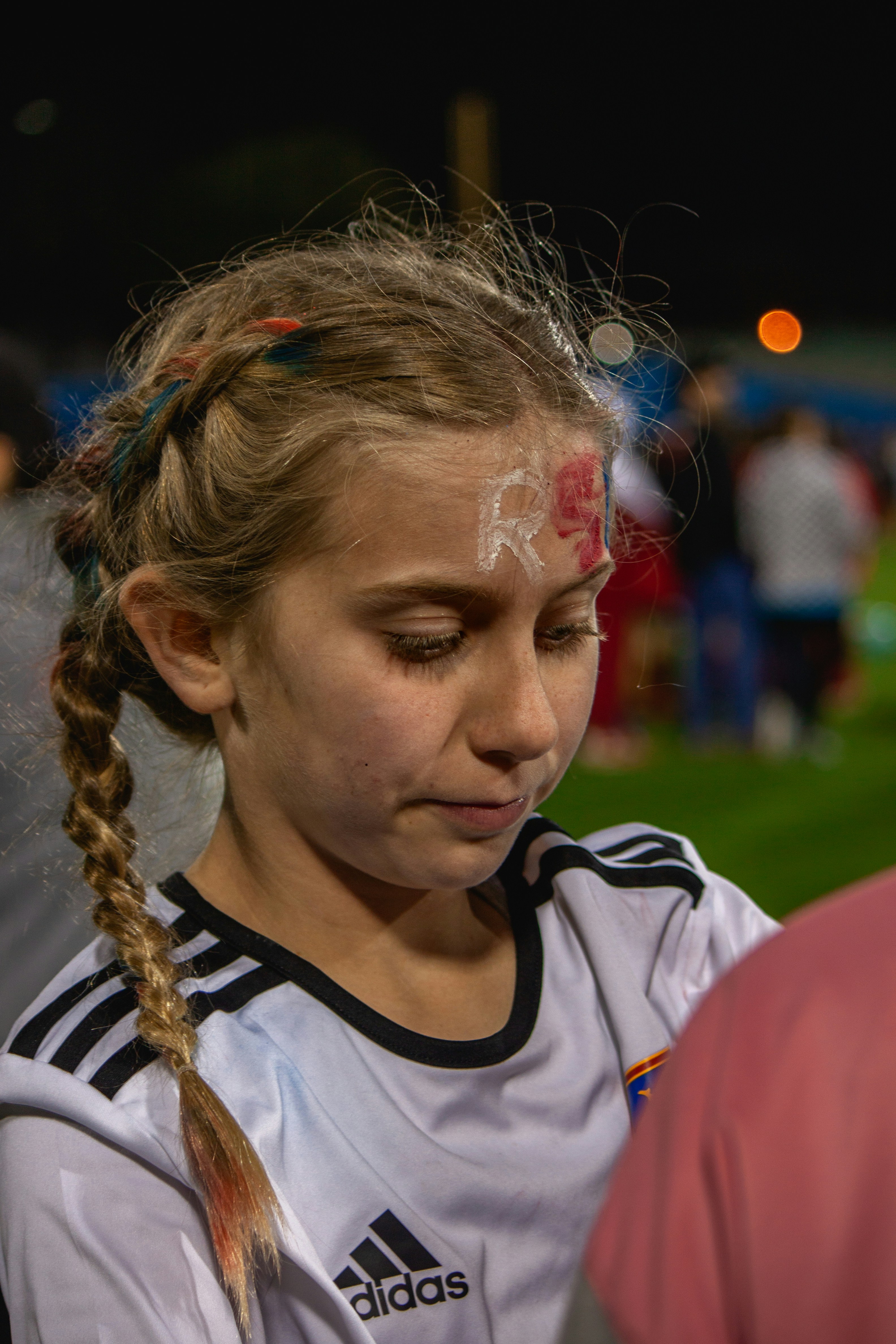 Painted Resolve: A girl with face paint curls into a quiet moment on the field
