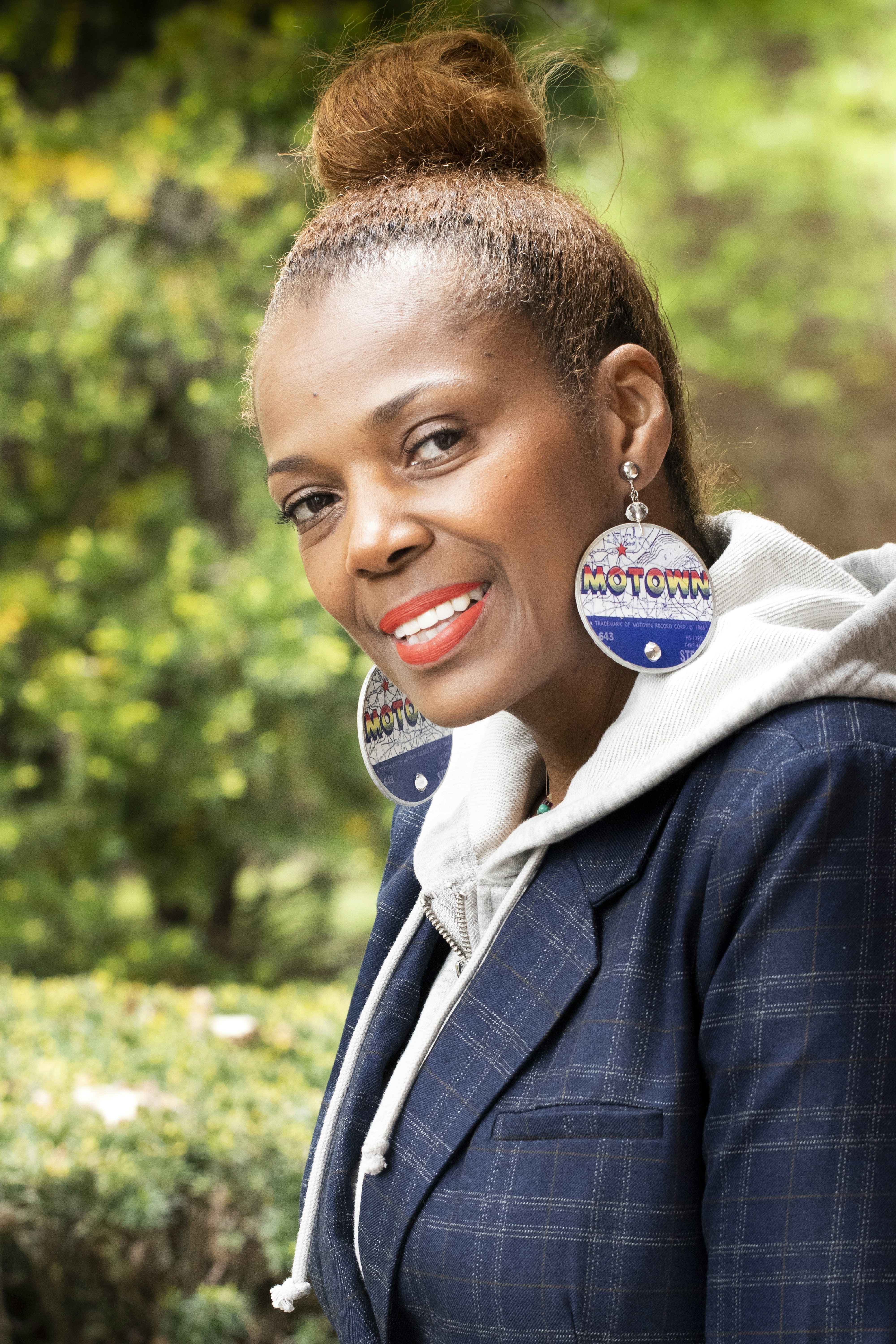 Woman in blue plaid jacket smiling against a lush green backdrop.