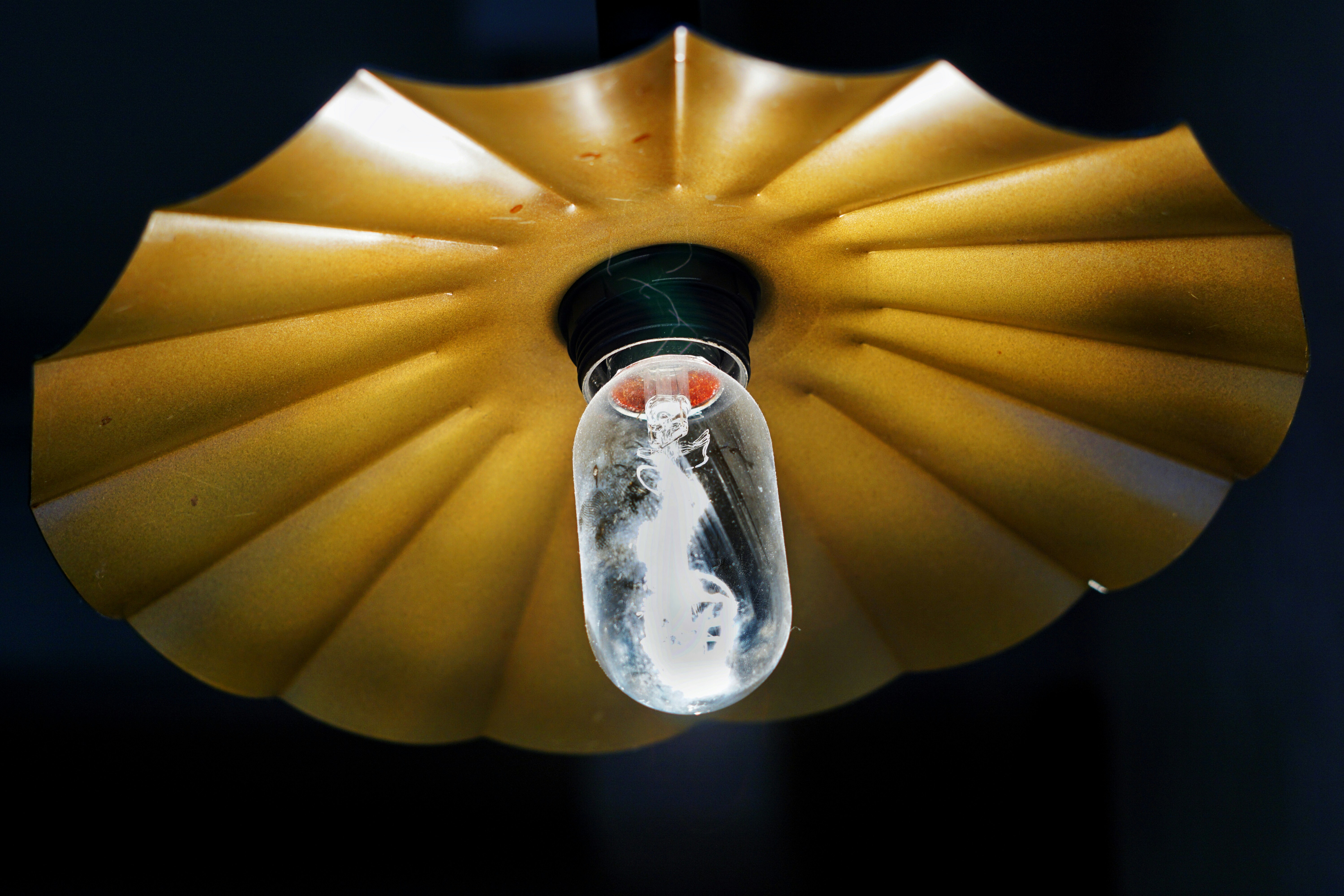 A vintage light fixture with a fluted yellow shade and a clear bulb, showcasing intricate details and a soft glow against a dark background.