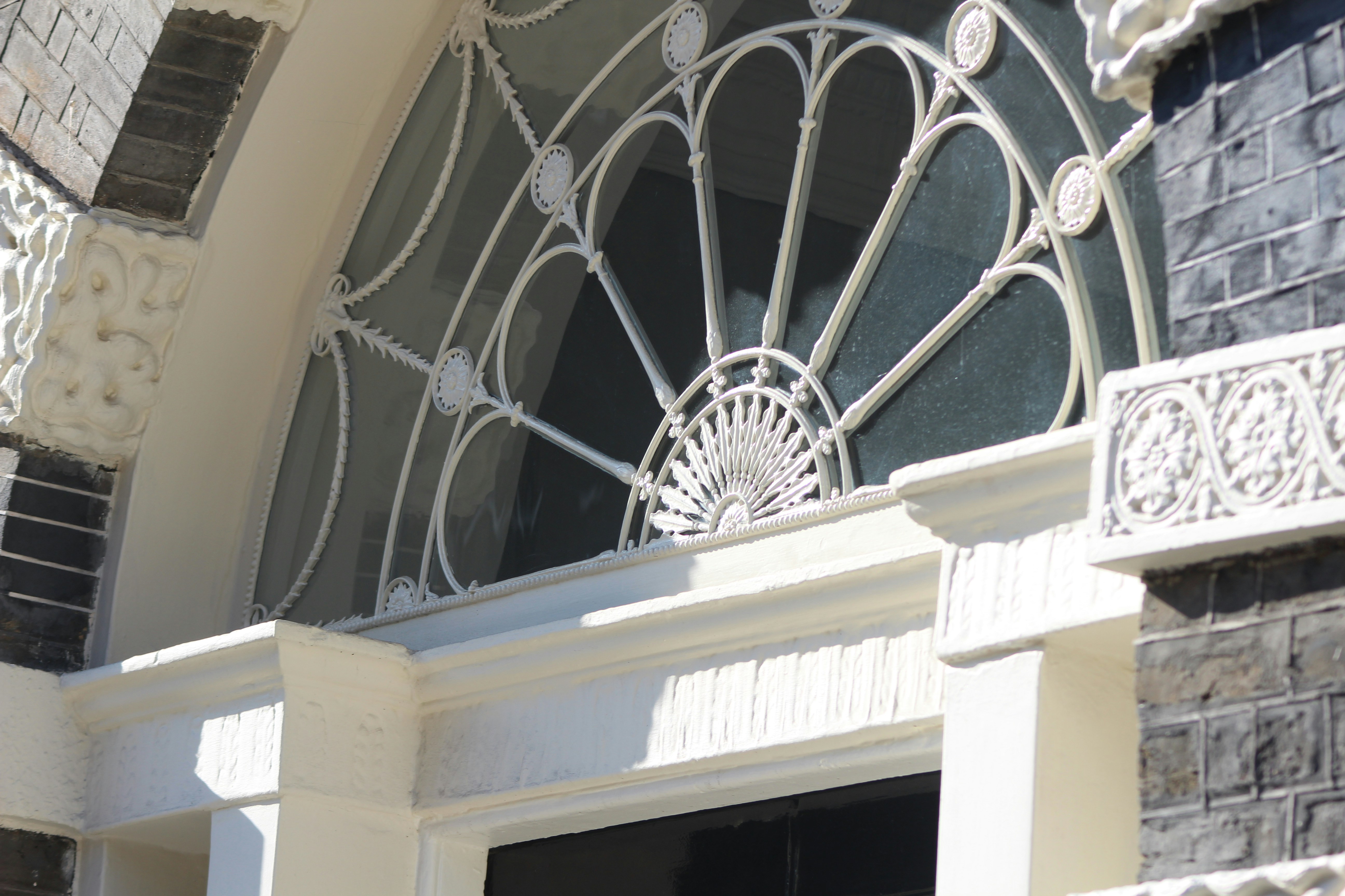 Circular Ironwork Fanlight Framed by White Portico in Sunlit Brick Facade