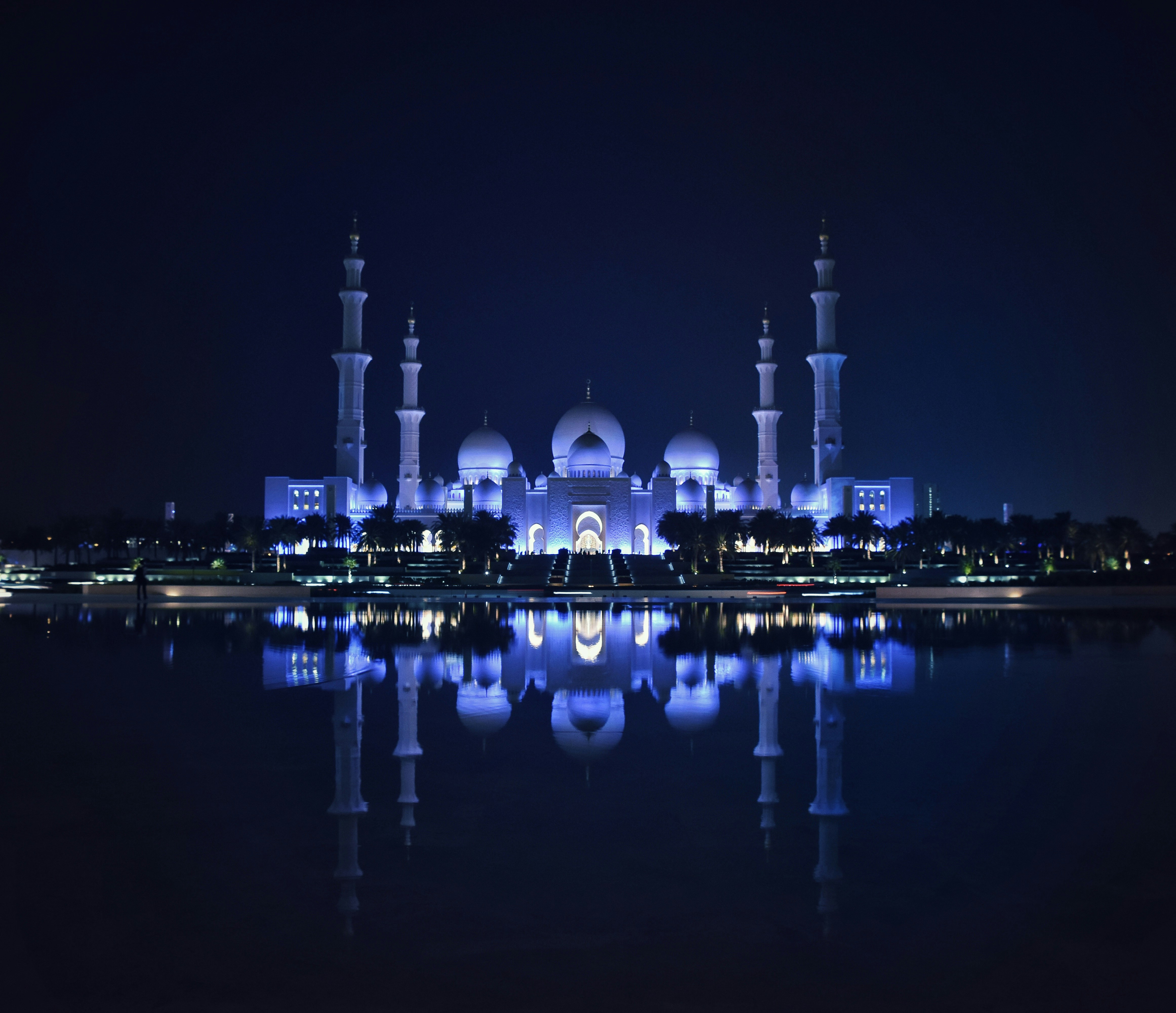 Sheikh Zayed Grand Mosque illuminated at night, mirrored perfectly in the calm water.