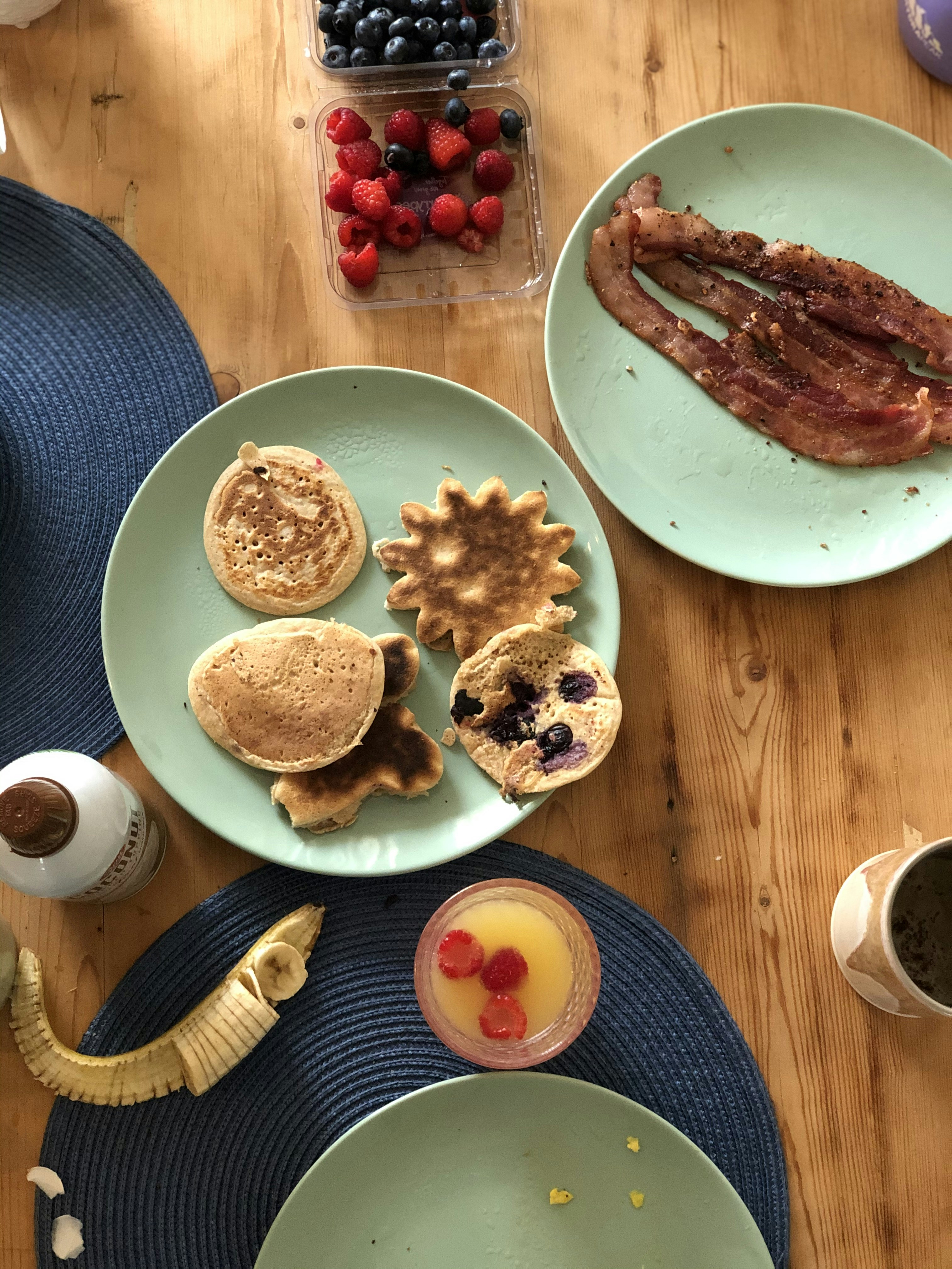 A delightful breakfast scene featuring pancakes, bacon, fresh berries, and a banana peel on a wooden table. The colorful arrangement invites a cozy dining experience.