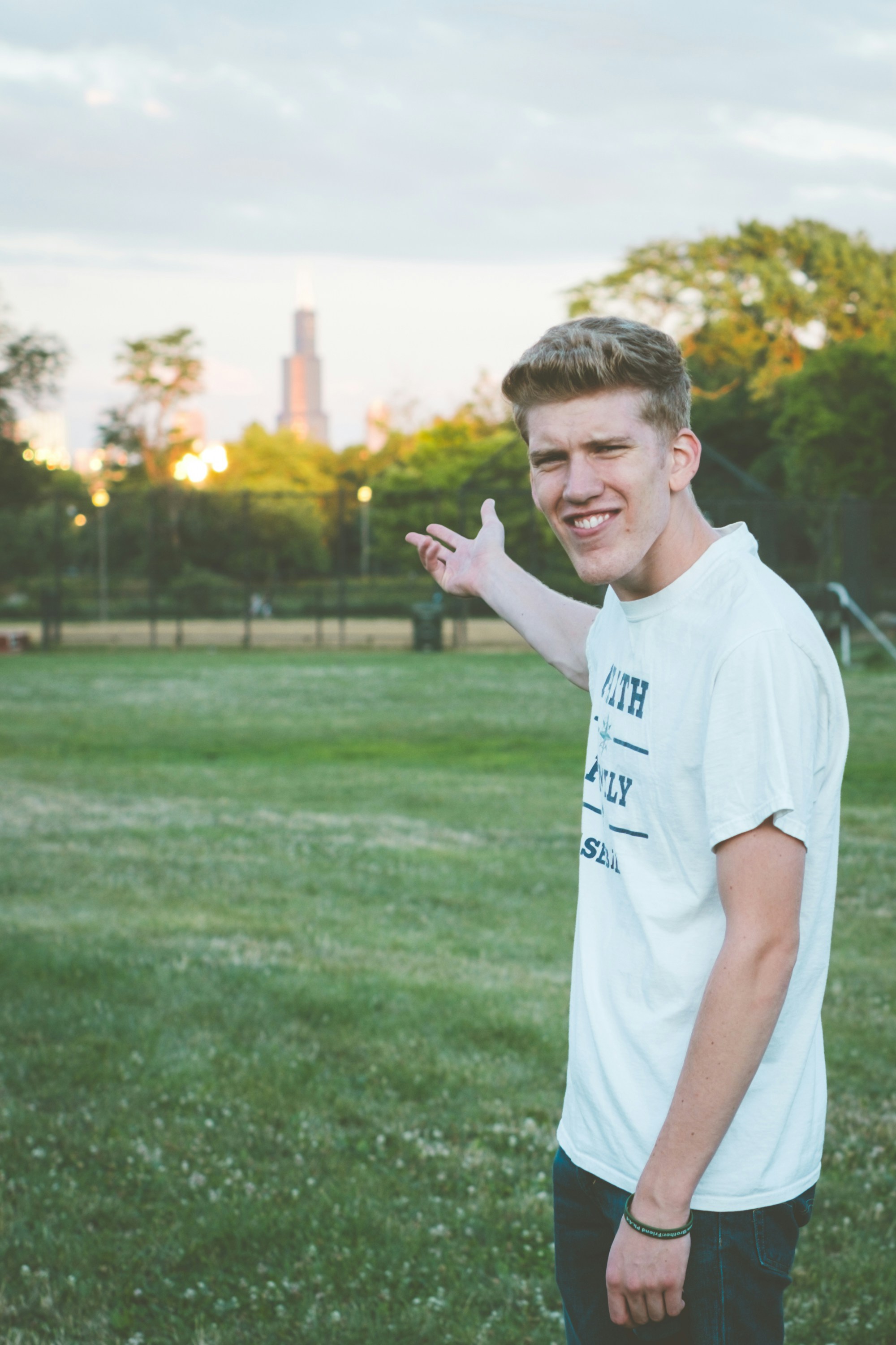 Man in a white t-shirt gestures towards a distant skyline under a cloudy sky.