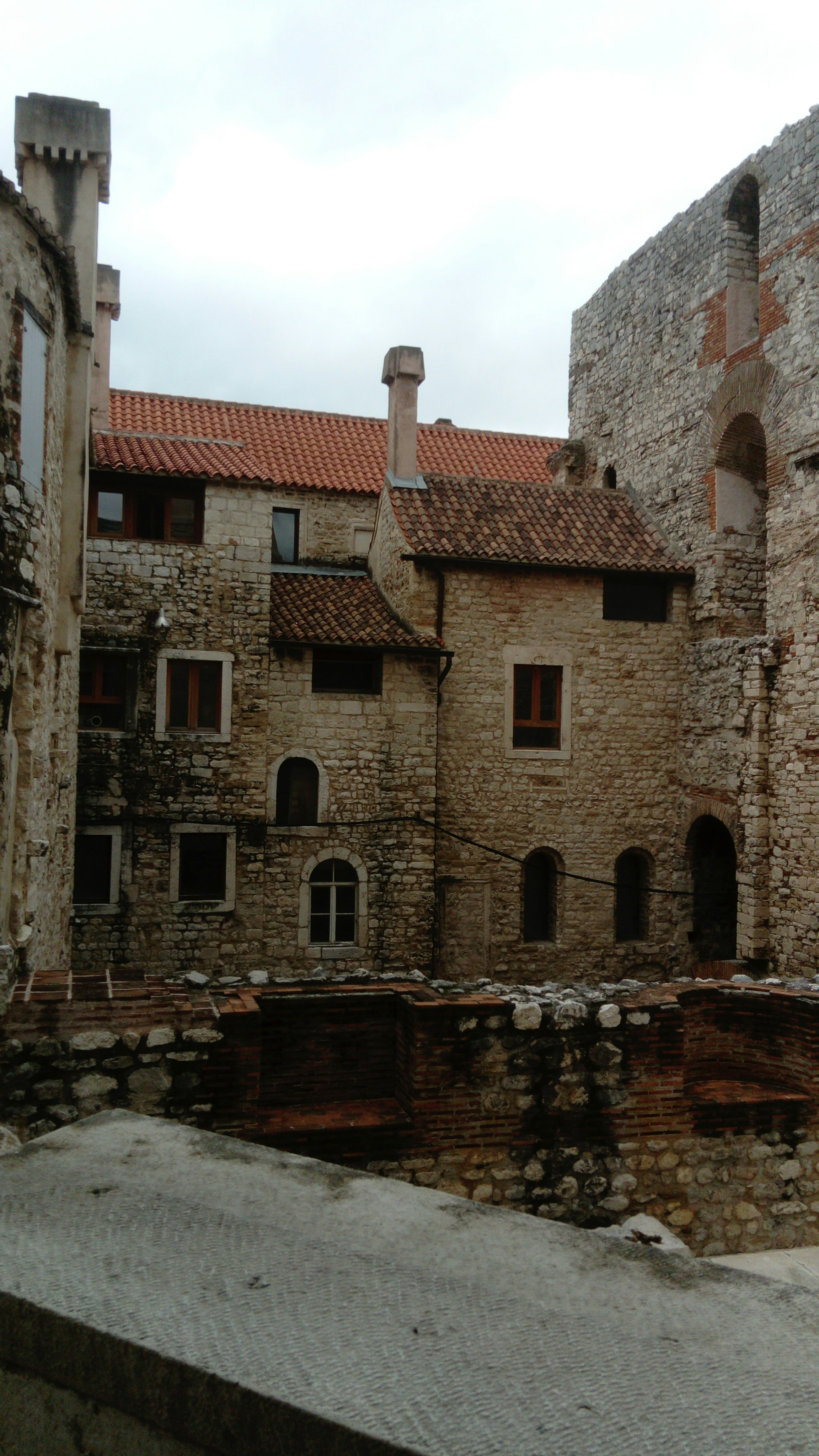 Ancient stone buildings with red-tiled roofs nestled within a courtyard, showcasing a blend of architectural styles and historical textures.