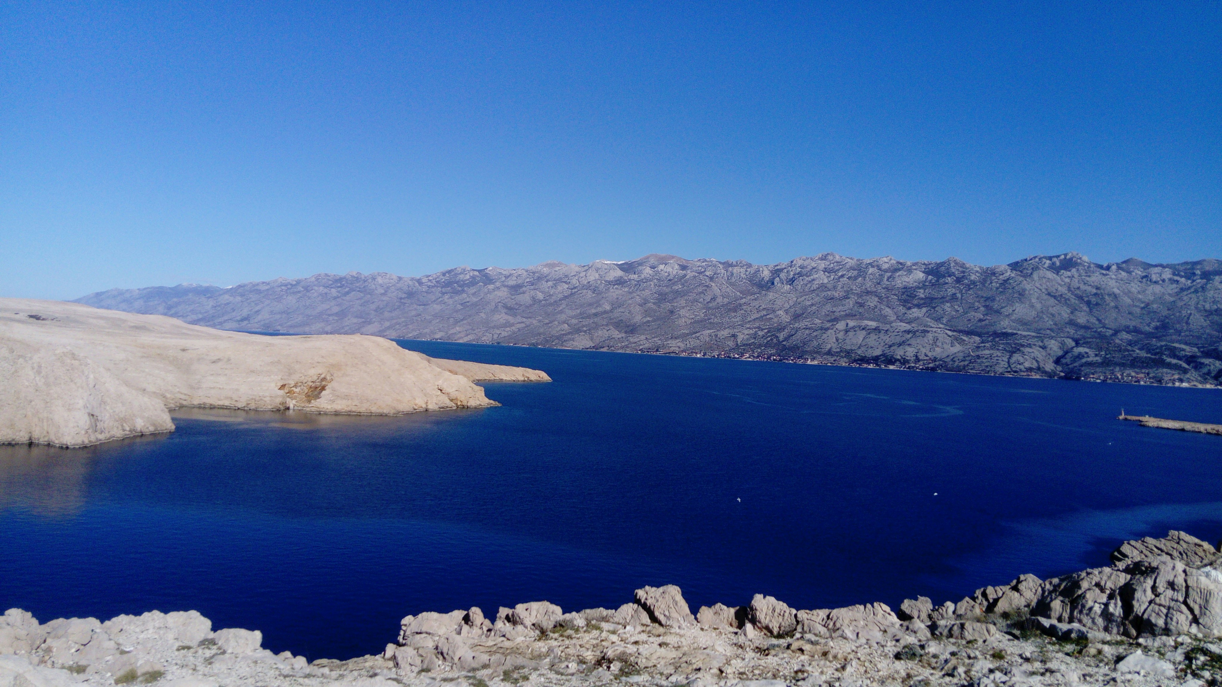 Vivid turquoise waters meet arid hills under a clear blue sky near Zadar, Croatia.