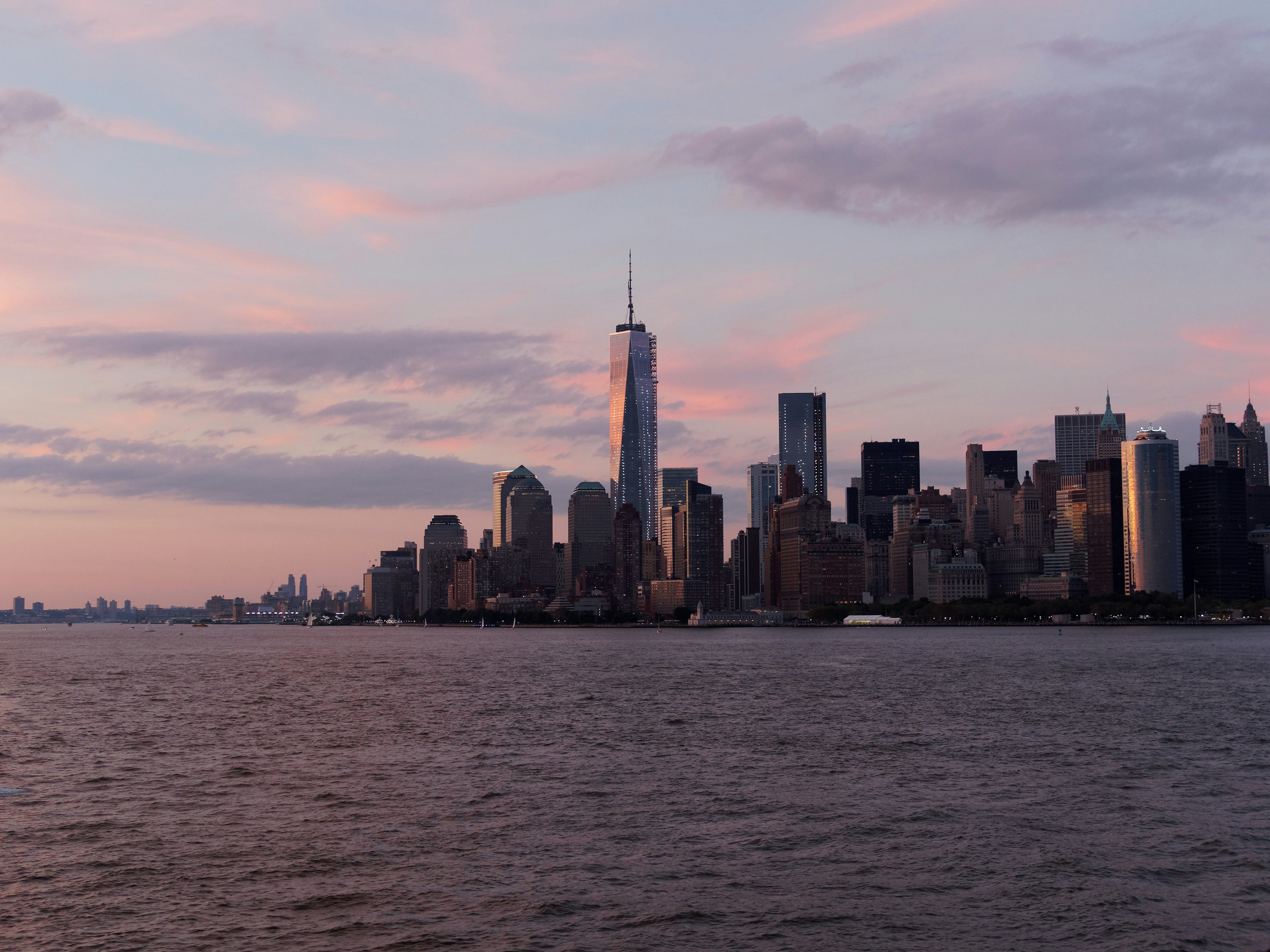 Skyscrapers silhouetted against a pastel dawn sky above rippling water.