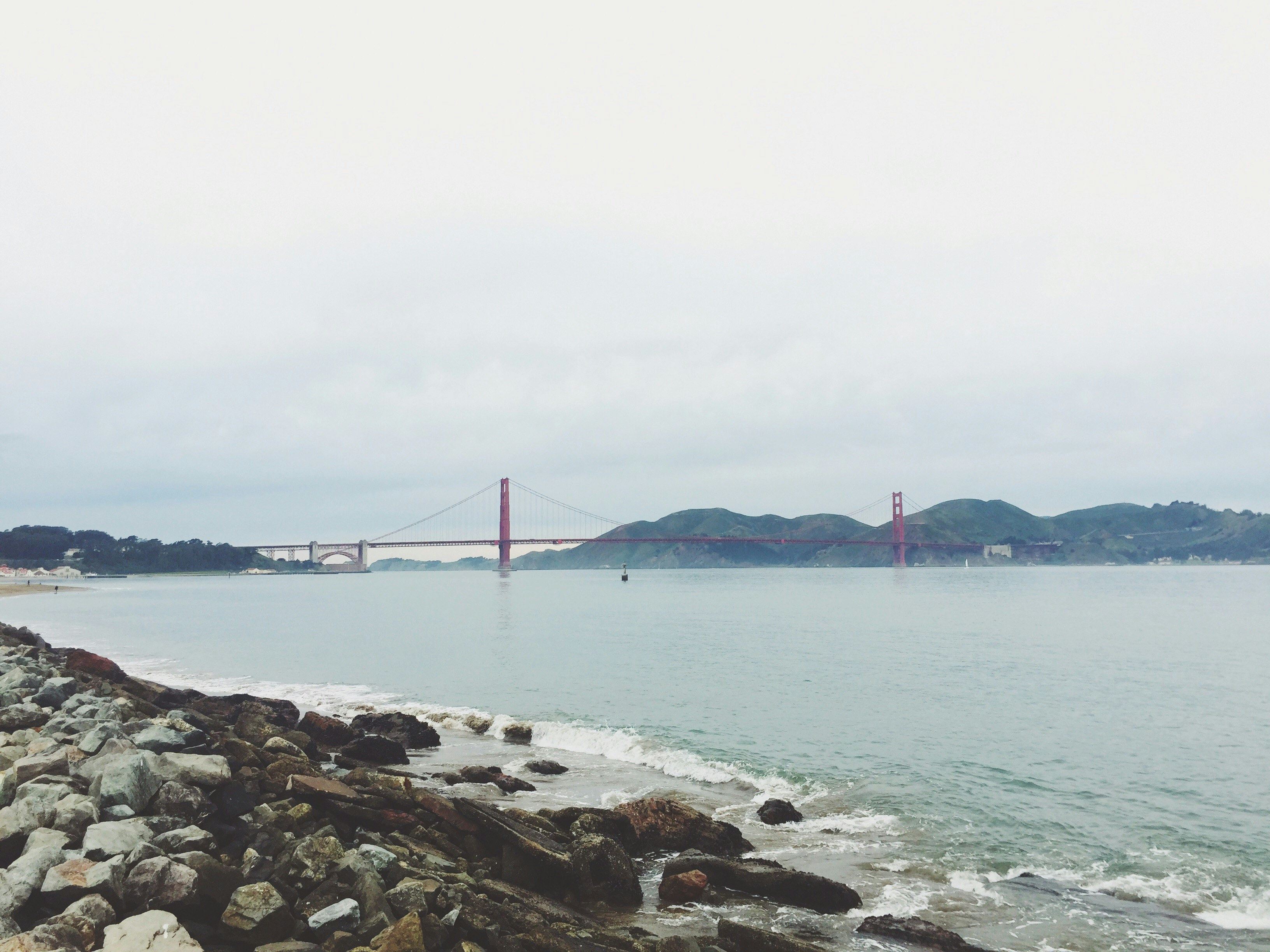 Red Span at the Quiet Bay: A Distant Bridge Framed by Rugged Shoreline