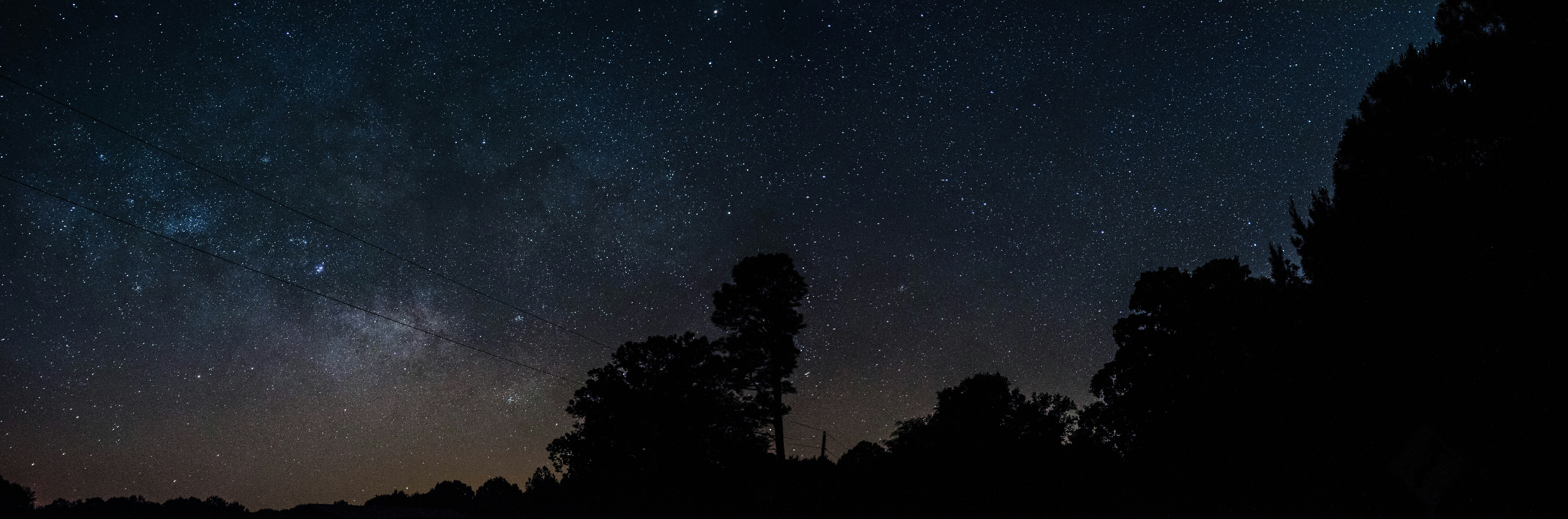 Star-filled night sky above a darkened forest silhouette.