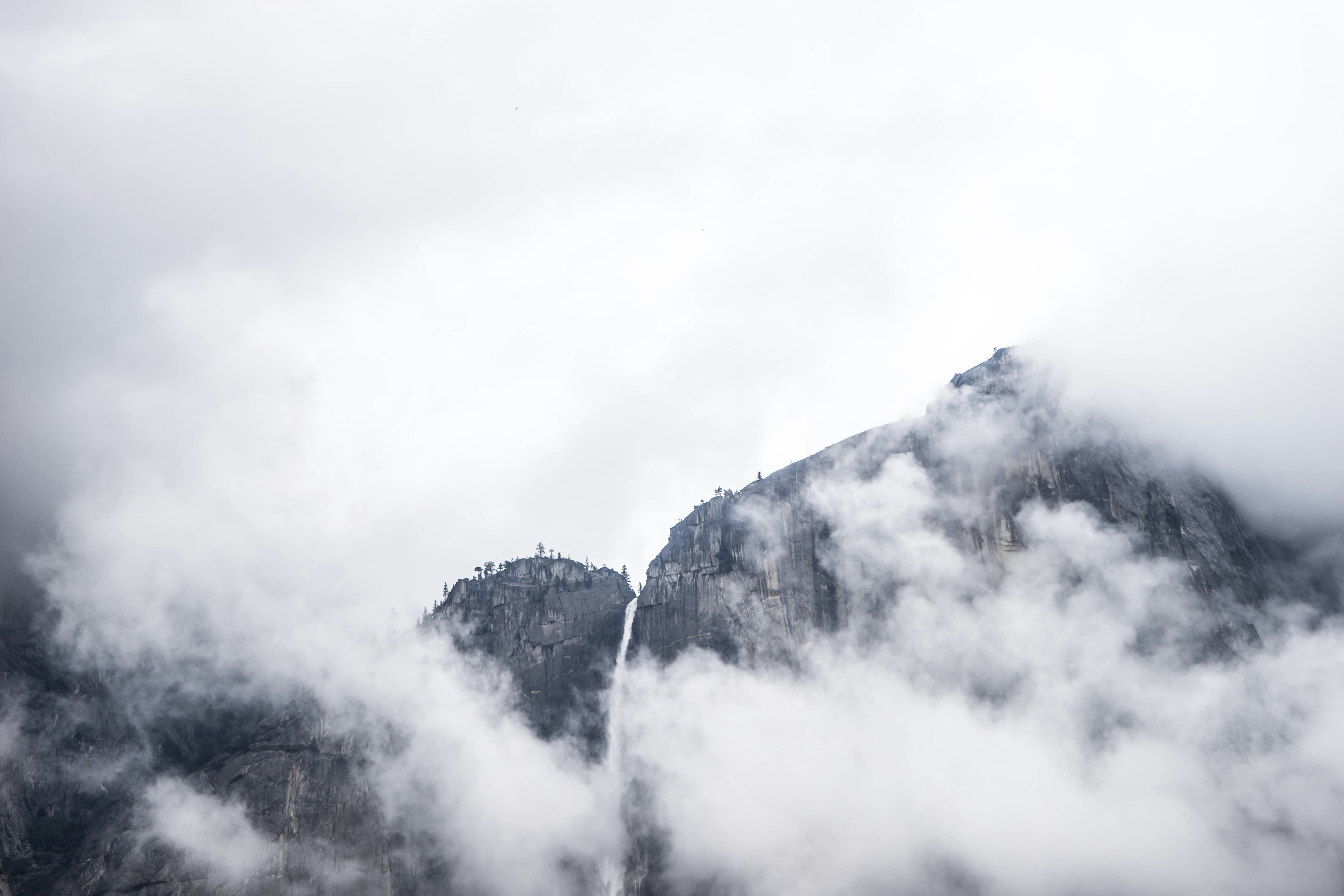 Misty clouds enveloping towering cliffs with a waterfall cascading down the rock face.