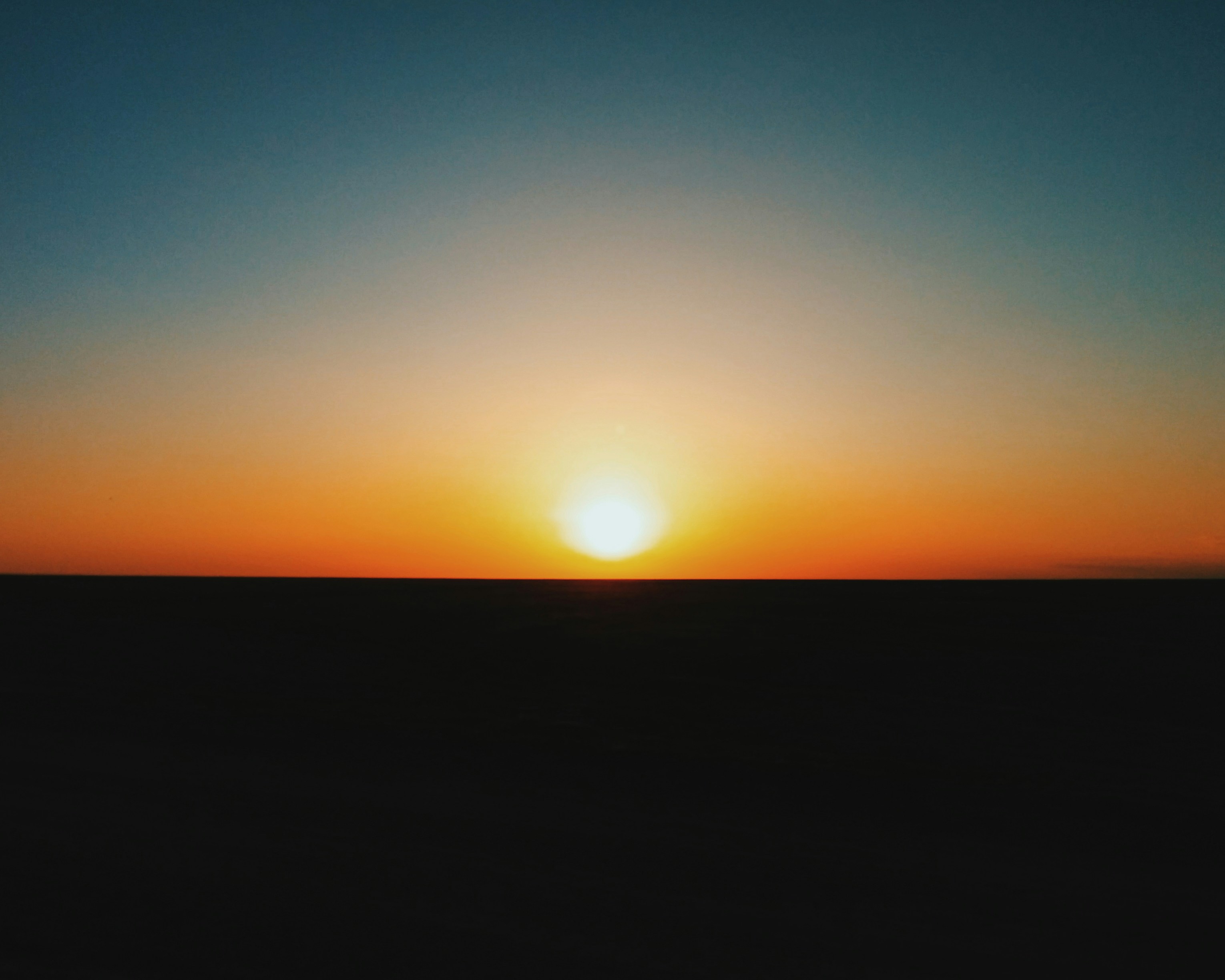 Vibrant sunset casting warm hues across the horizon, blending orange and blue tones. The scene captures the serene transition from day to night.