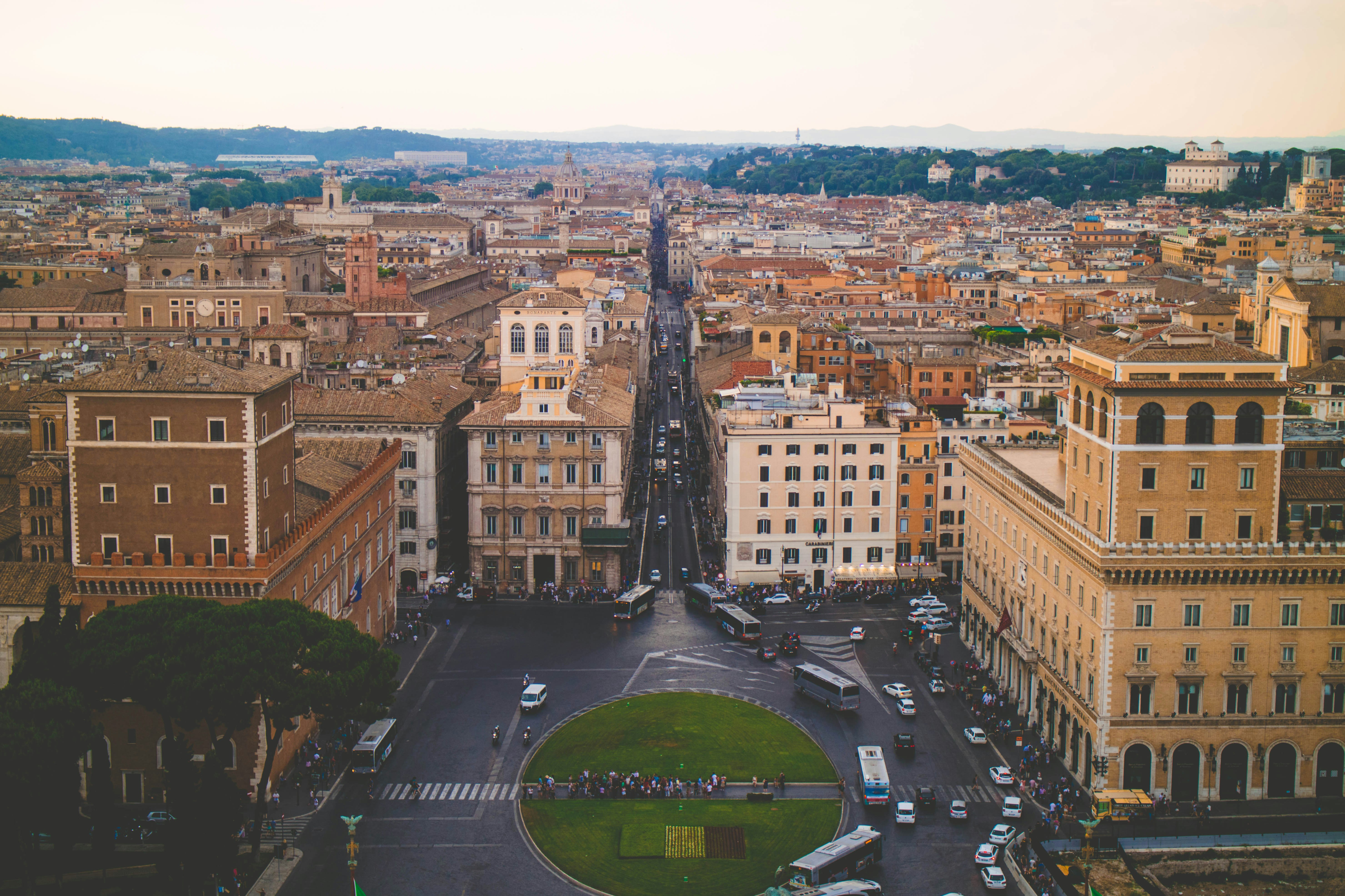Aerial view of a vast urban landscape with a central roundabout, flanked by historic buildings under a soft evening sky.