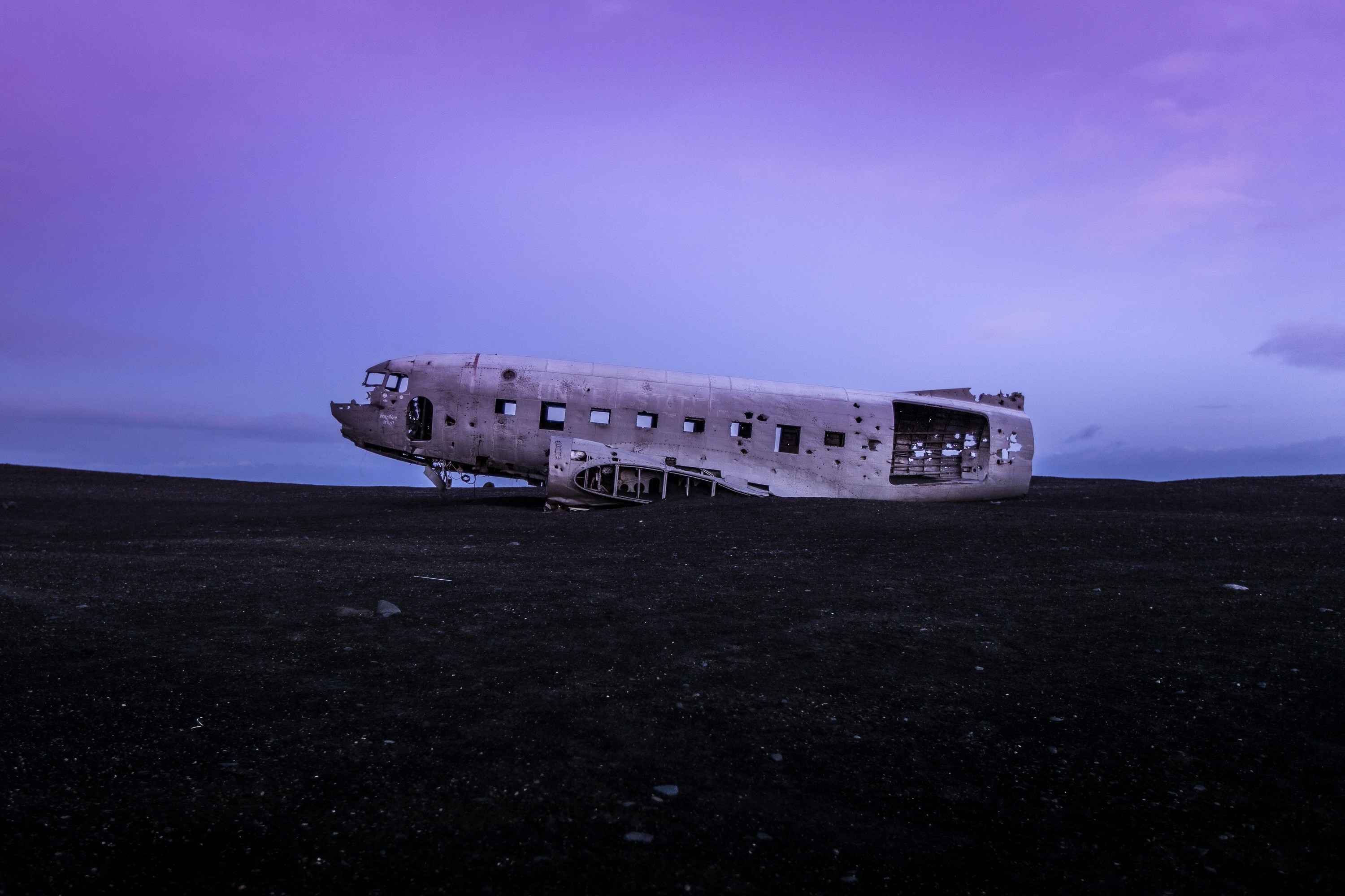 Abandoned airplane fuselage resting on a desolate landscape under a twilight sky.