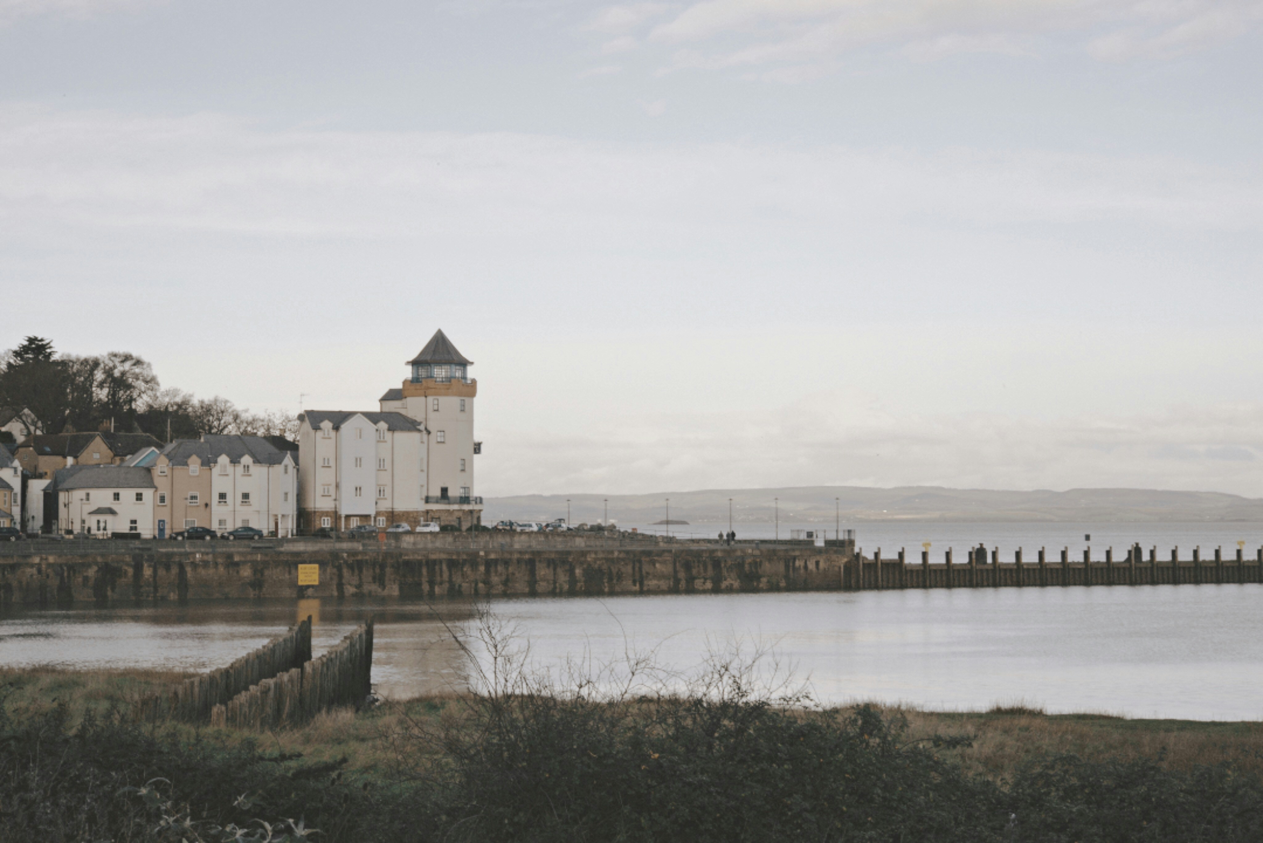 Coastal buildings line the harbor, with a distinctive tower marking the skyline against a calm sea. The soft light enhances the tranquil atmosphere.