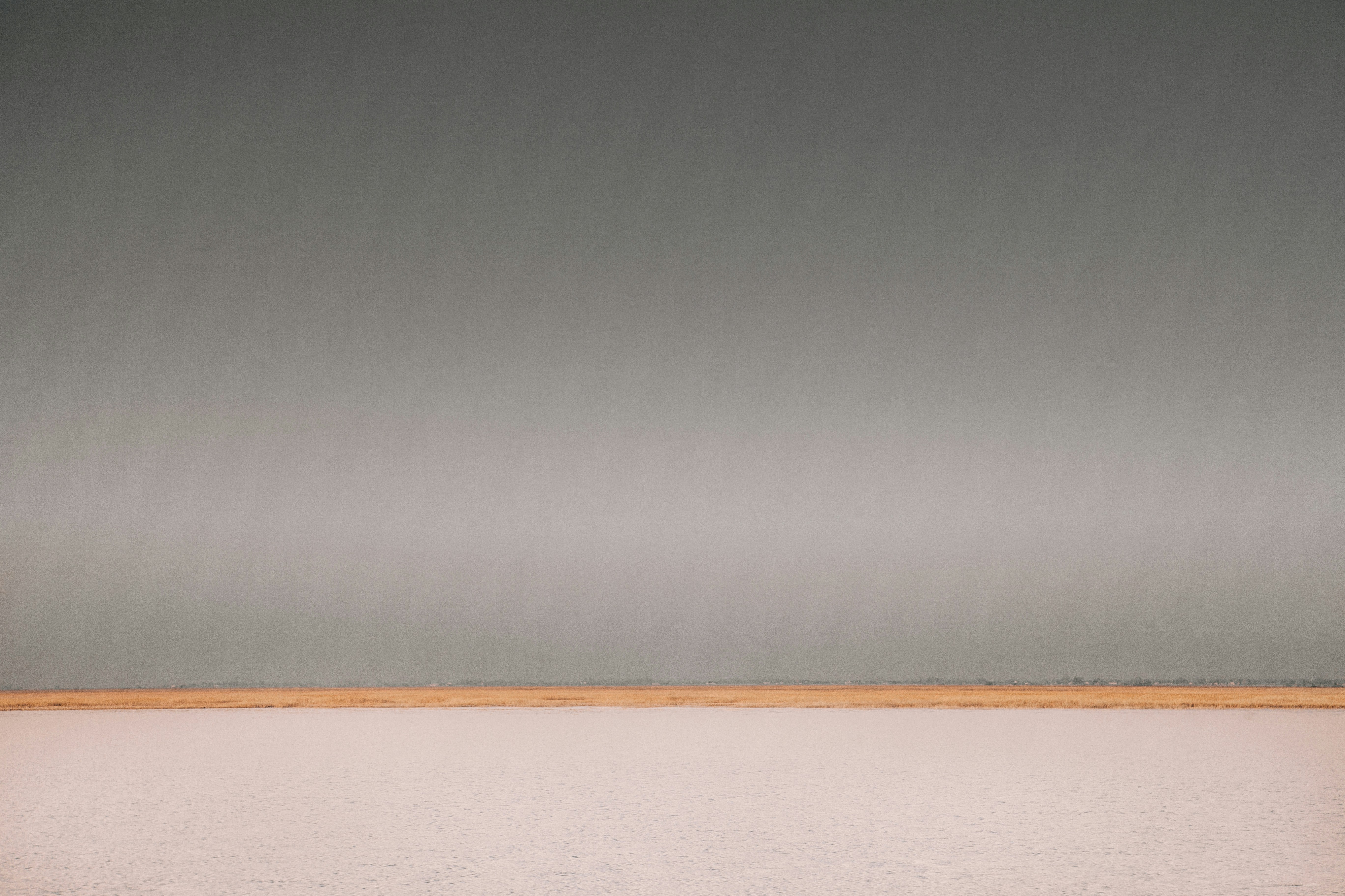A serene landscape featuring a subtle gradient sky above a calm, reflective surface, with a thin golden strip of land on the horizon.