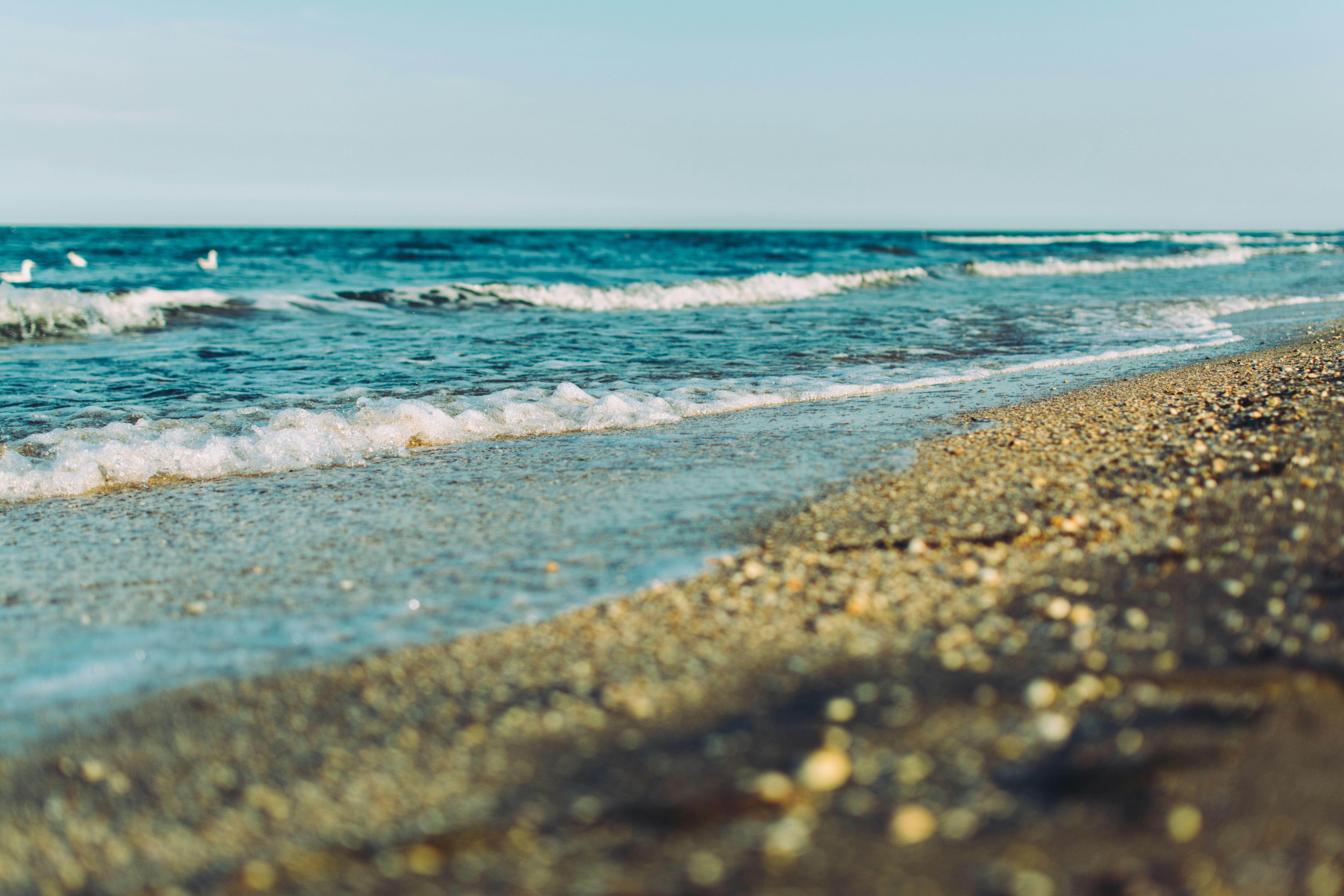 Waves gently lap against a pebbled shoreline under a clear blue sky.