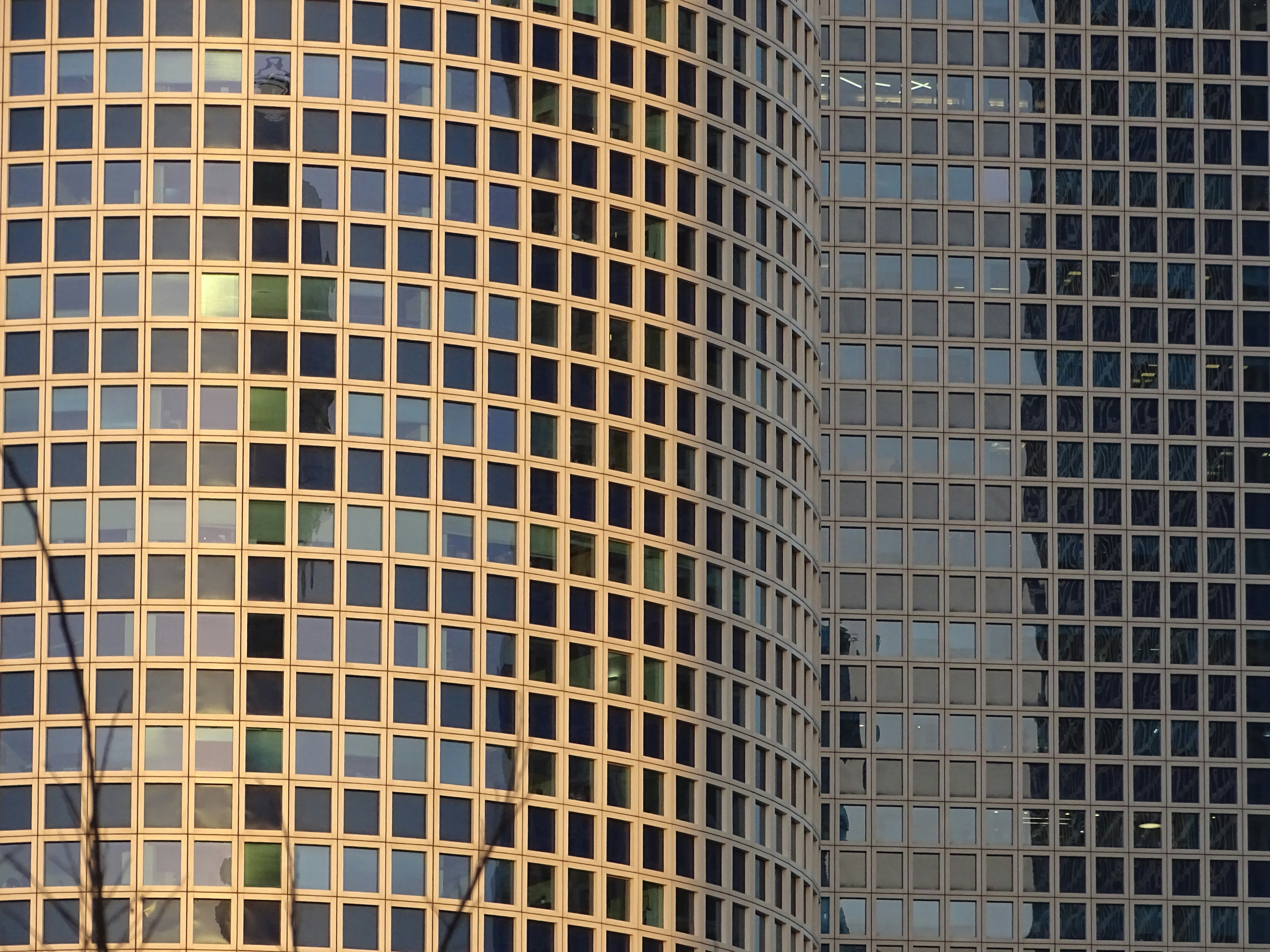 Curved glass facades of modern skyscrapers reflect sunlight, creating a grid pattern of light and shadow.