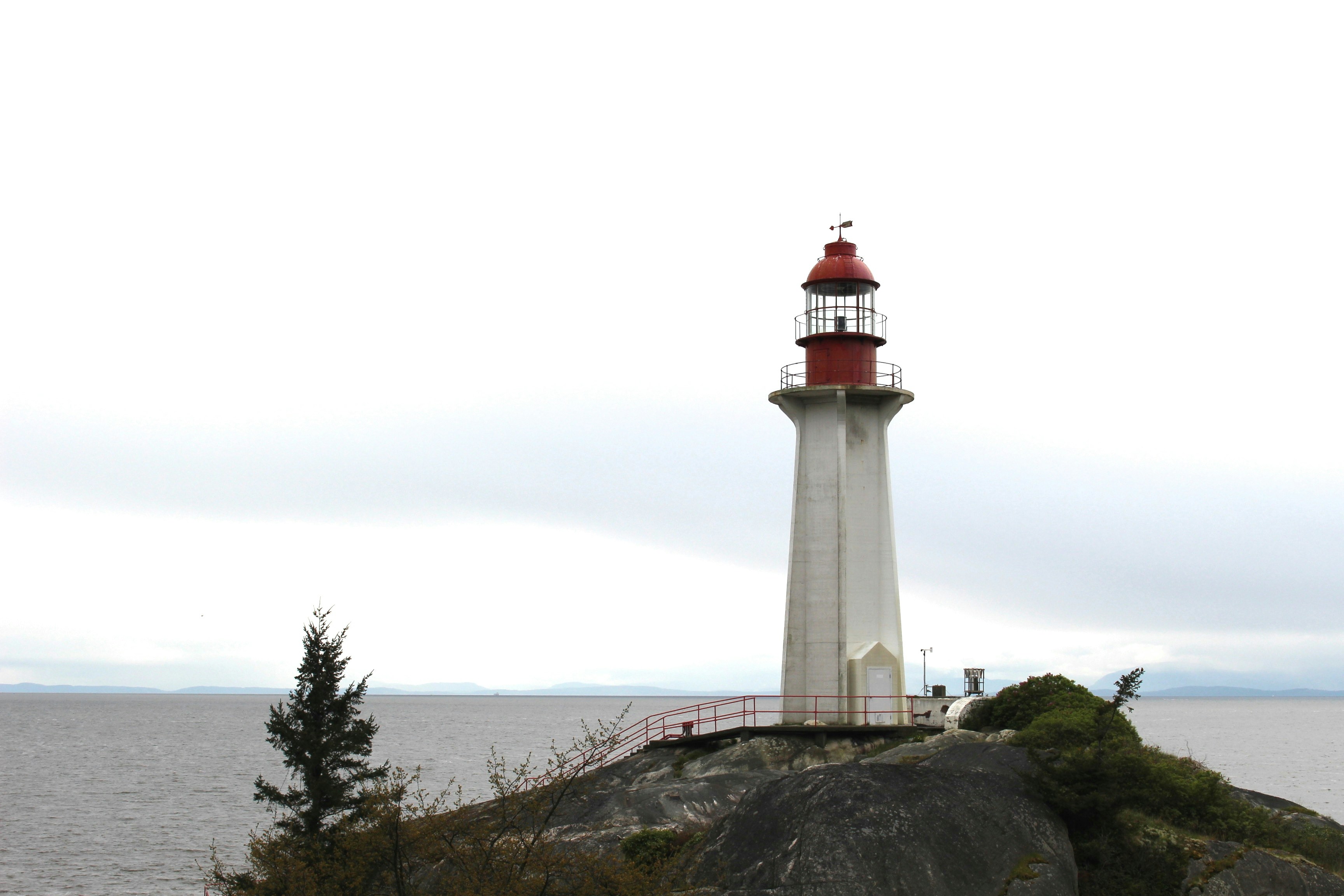 A lighthouse stands resolutely on a rocky outcrop, overlooking a calm sea under a cloudy sky. The structure's red and white colors contrast with the muted tones of the landscape.