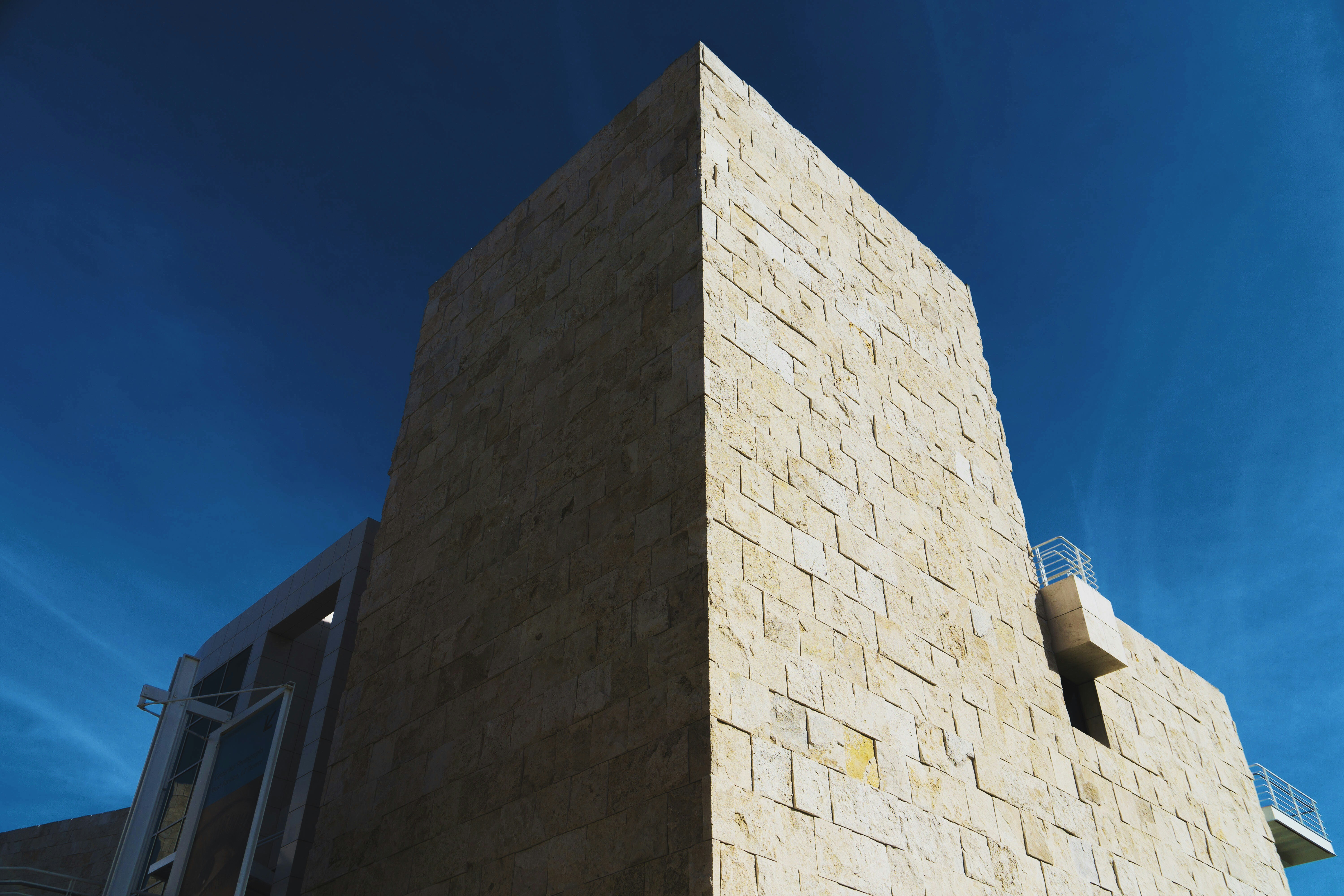 A modern architectural structure with a textured stone facade rises sharply against a vibrant blue sky, showcasing a blend of natural and man-made elements.
