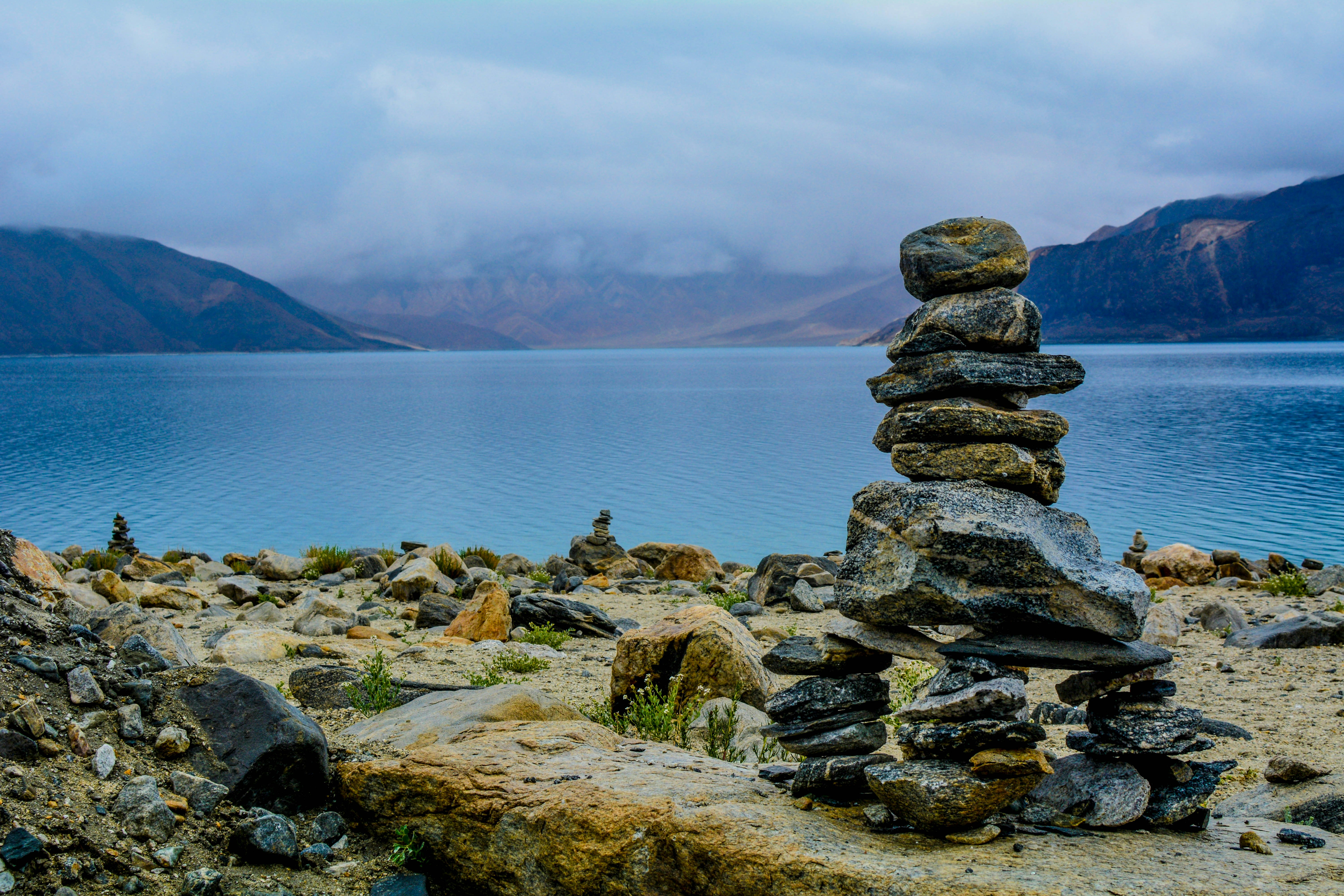 Stacked stones on a rocky shoreline with a tranquil lake and misty mountains in the background.