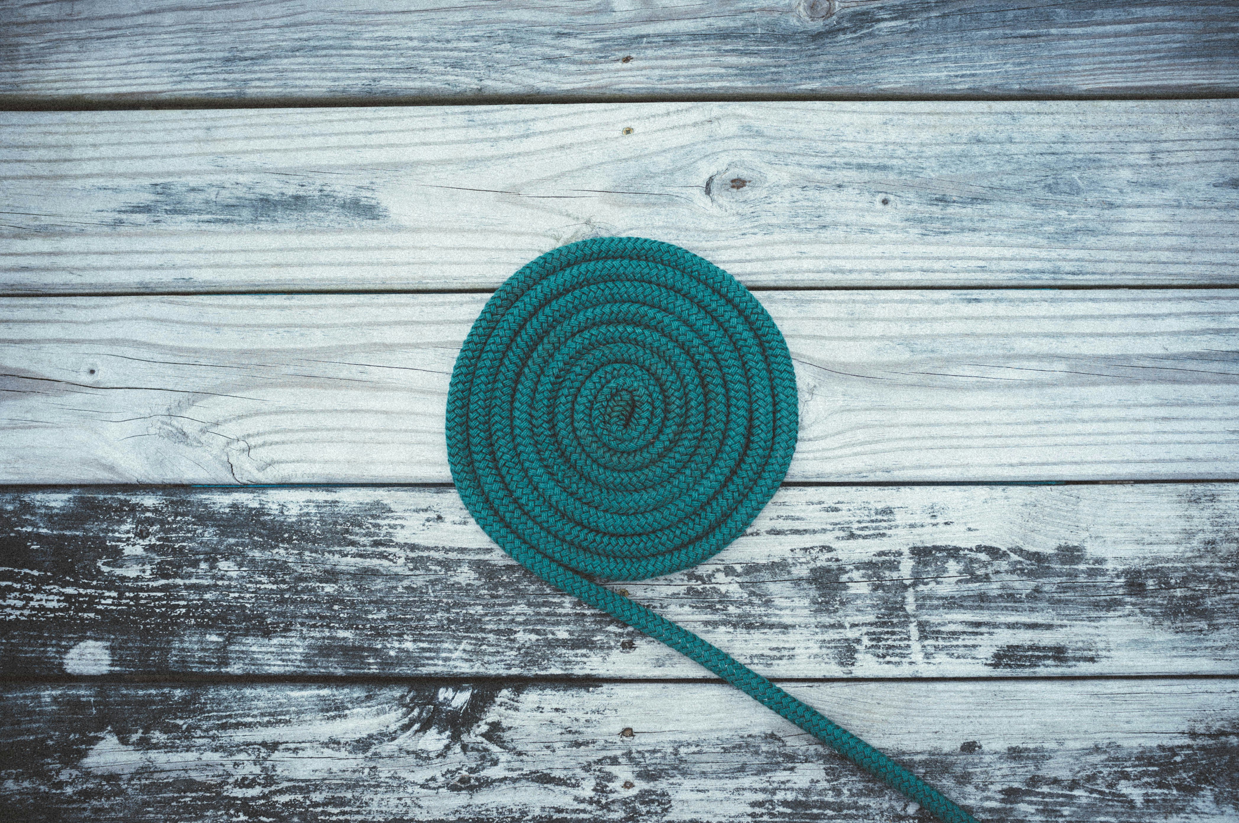 Teal rope coiled in a perfect spiral on weathered wooden planks, showcasing texture and color contrasts.