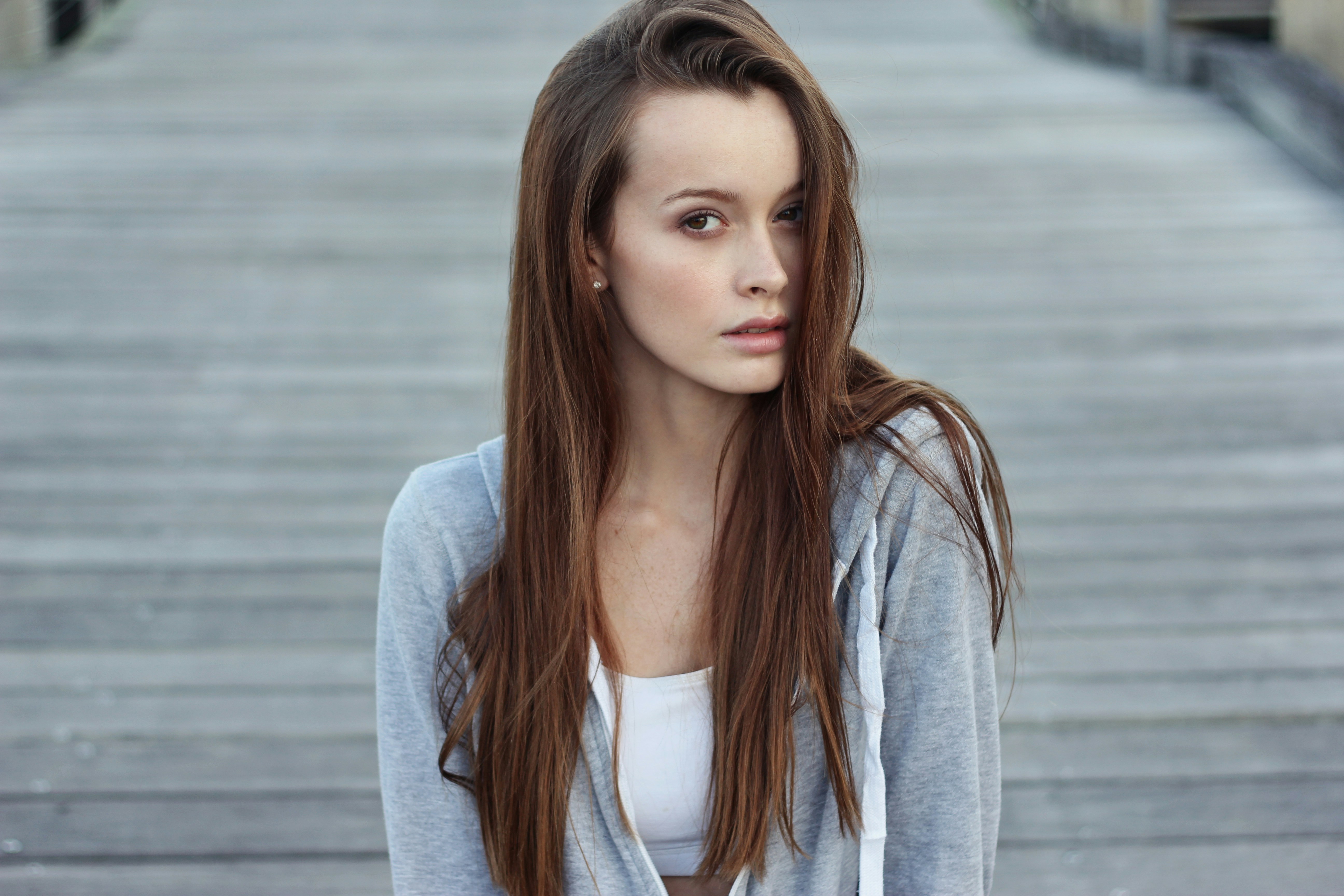Young woman with long hair gazing thoughtfully while seated on a wooden boardwalk.