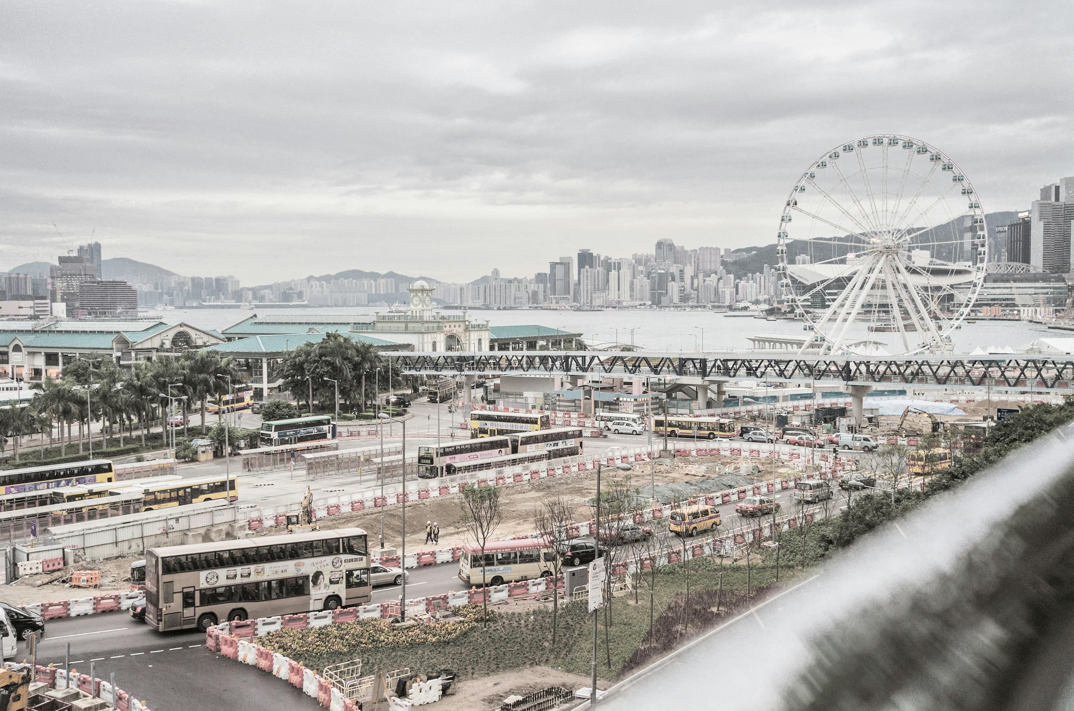 View of a bustling urban landscape featuring a ferris wheel, busy roads, and distant skyscrapers under a moody sky.