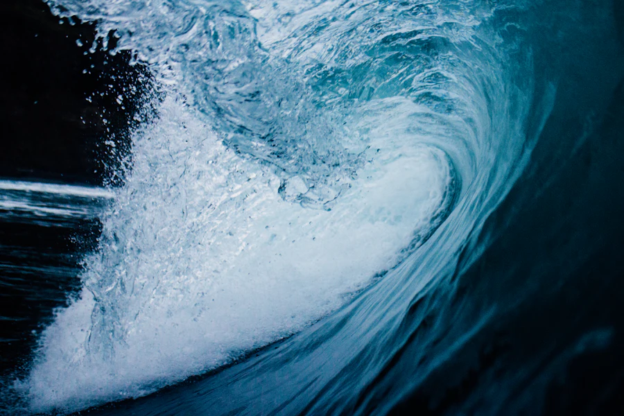 Close-up of a powerful ocean wave curling into a hollow barrel, with spray exploding along the left side and dark water framing the scene.